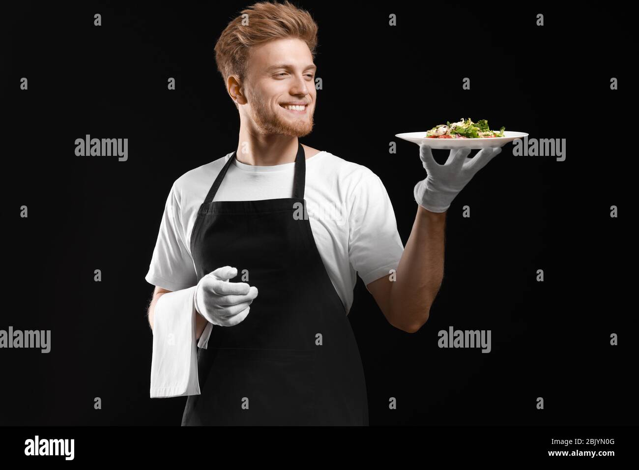 Handsome waiter with salad on dark background Stock Photo - Alamy