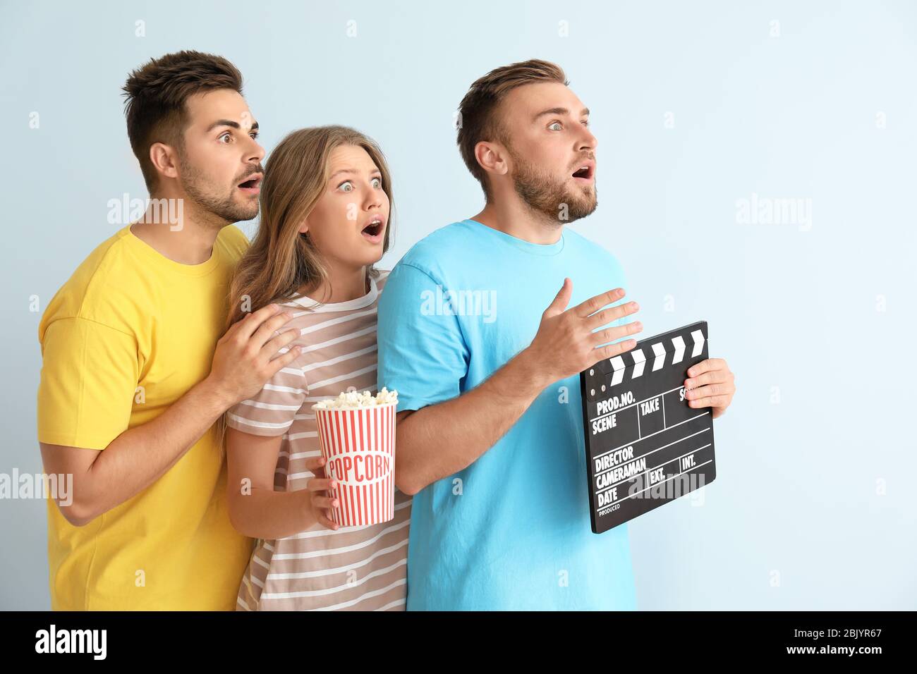 Shocked friends with popcorn and movie clapper on light background ...