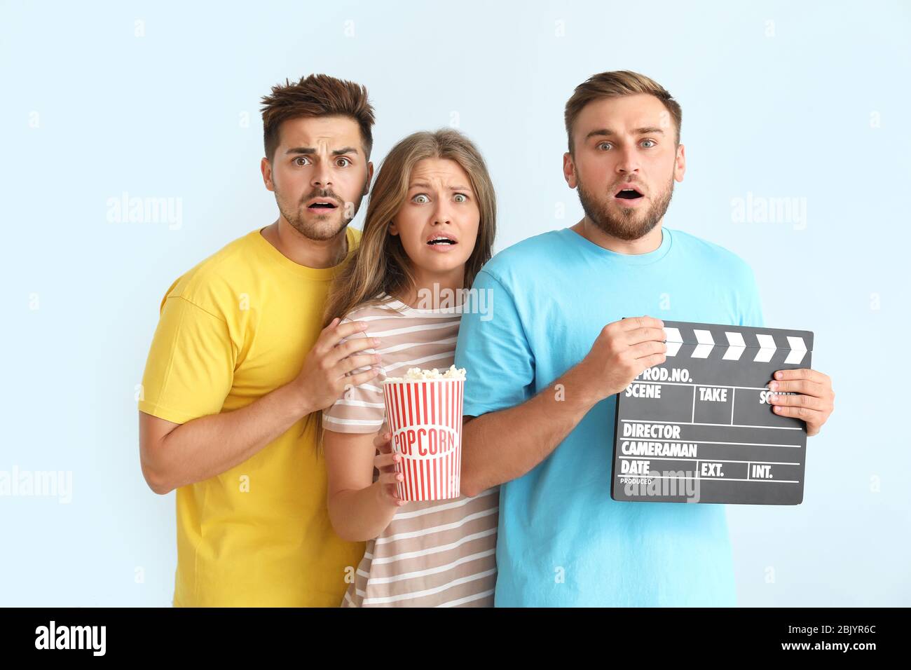 Scared friends with popcorn and movie clapper on light background Stock ...