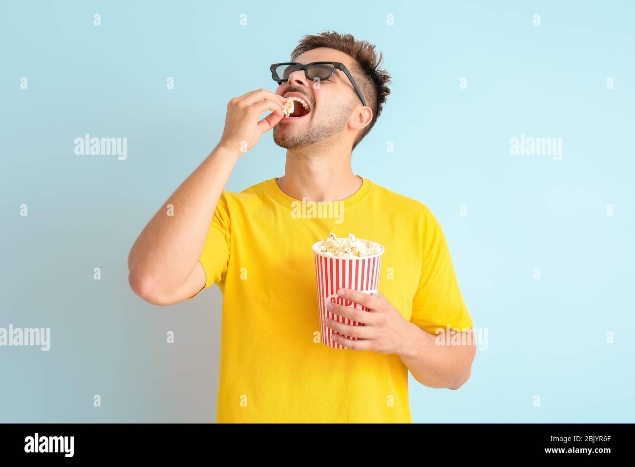 Young man eating popcorn on light background Stock Photo - Alamy