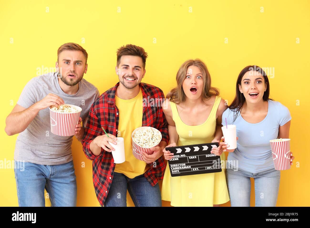 Emotional friends with popcorn and movie clapper on color background ...