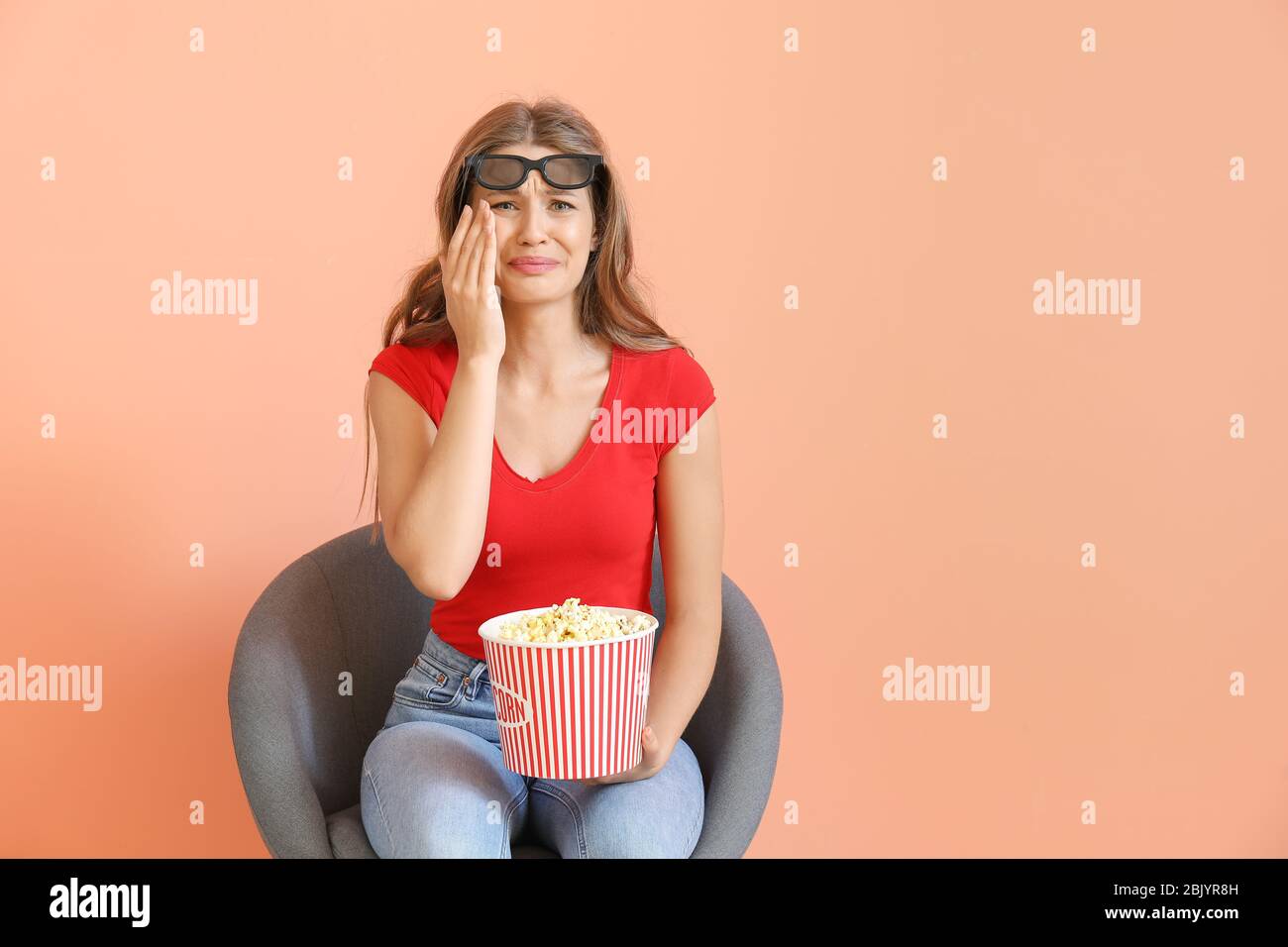 Crying woman with popcorn watching movie on color background Stock ...