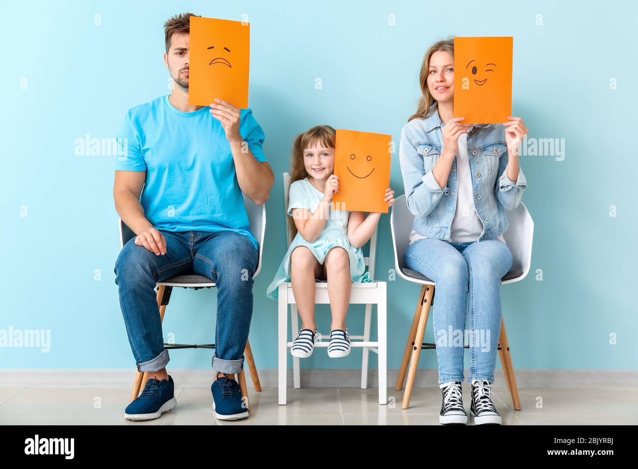 Young family with emoticons sitting on chairs near color wall Stock ...