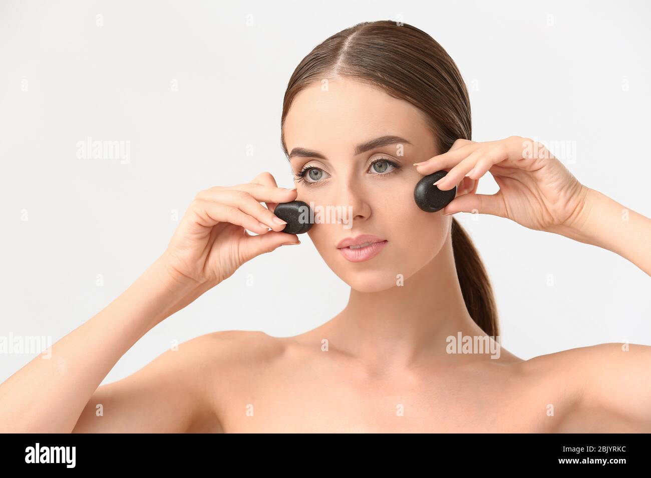 Beautiful woman massaging her face with hot stones white background ...