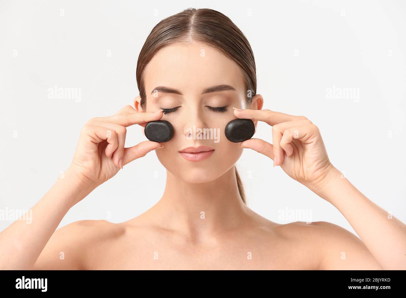 Beautiful woman massaging her face with hot stones white background ...