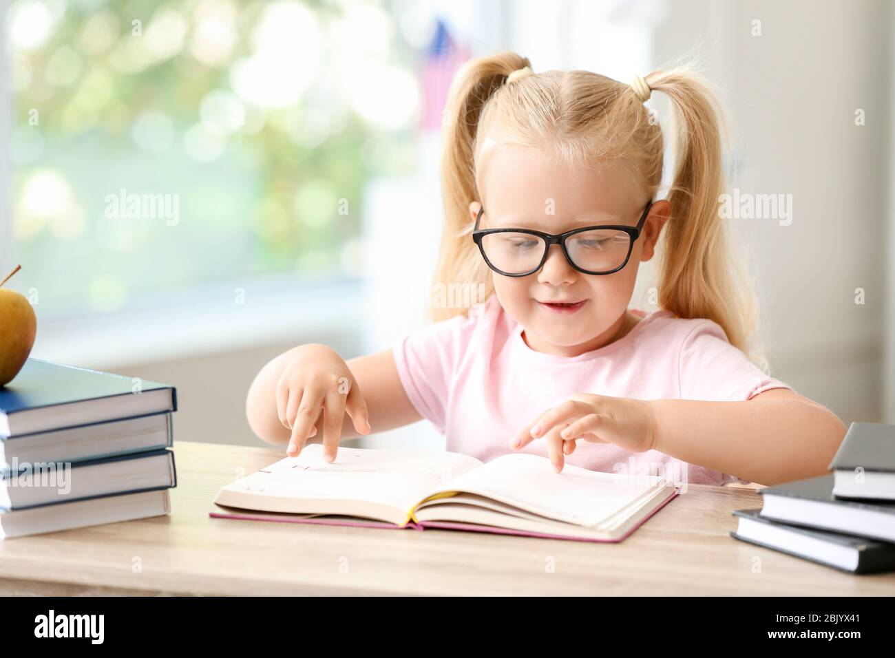 Cute little schoolgirl reading book at desk in classroom Stock Photo ...