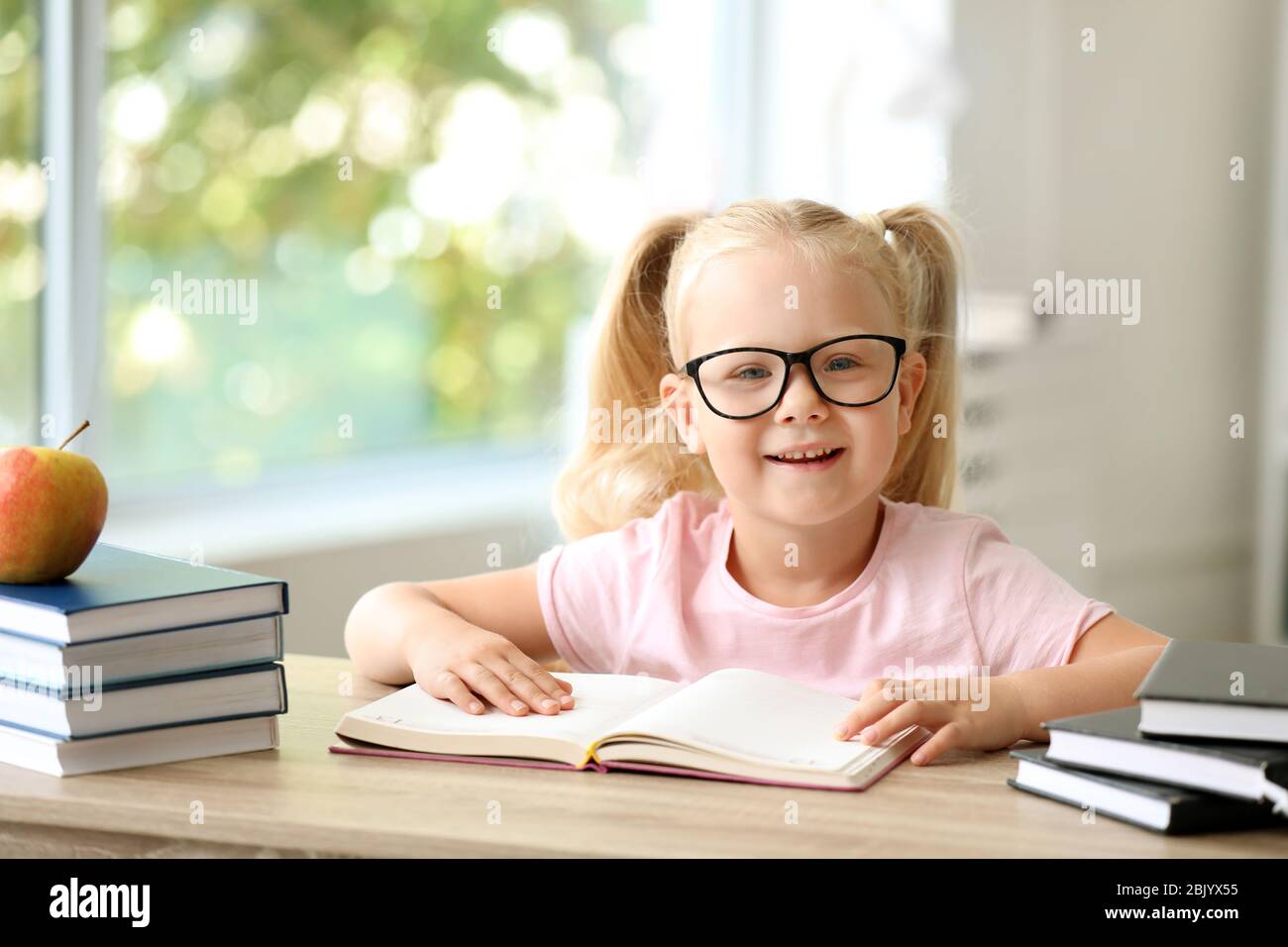 Cute little schoolgirl reading book at desk in classroom Stock Photo ...