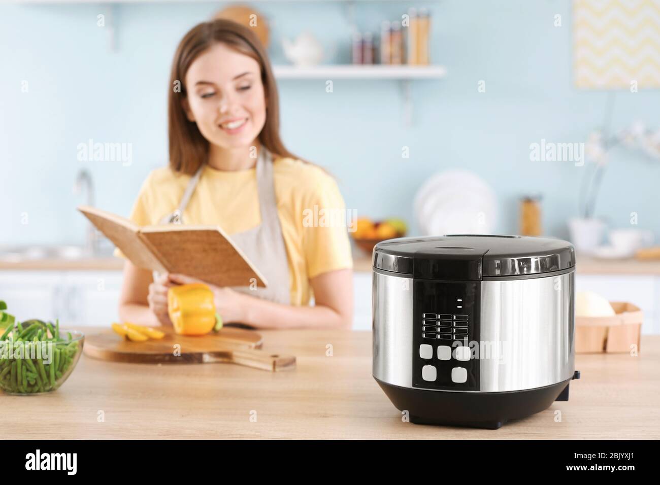 Woman with recipe book using modern multi cooker in kitchen Stock Photo ...