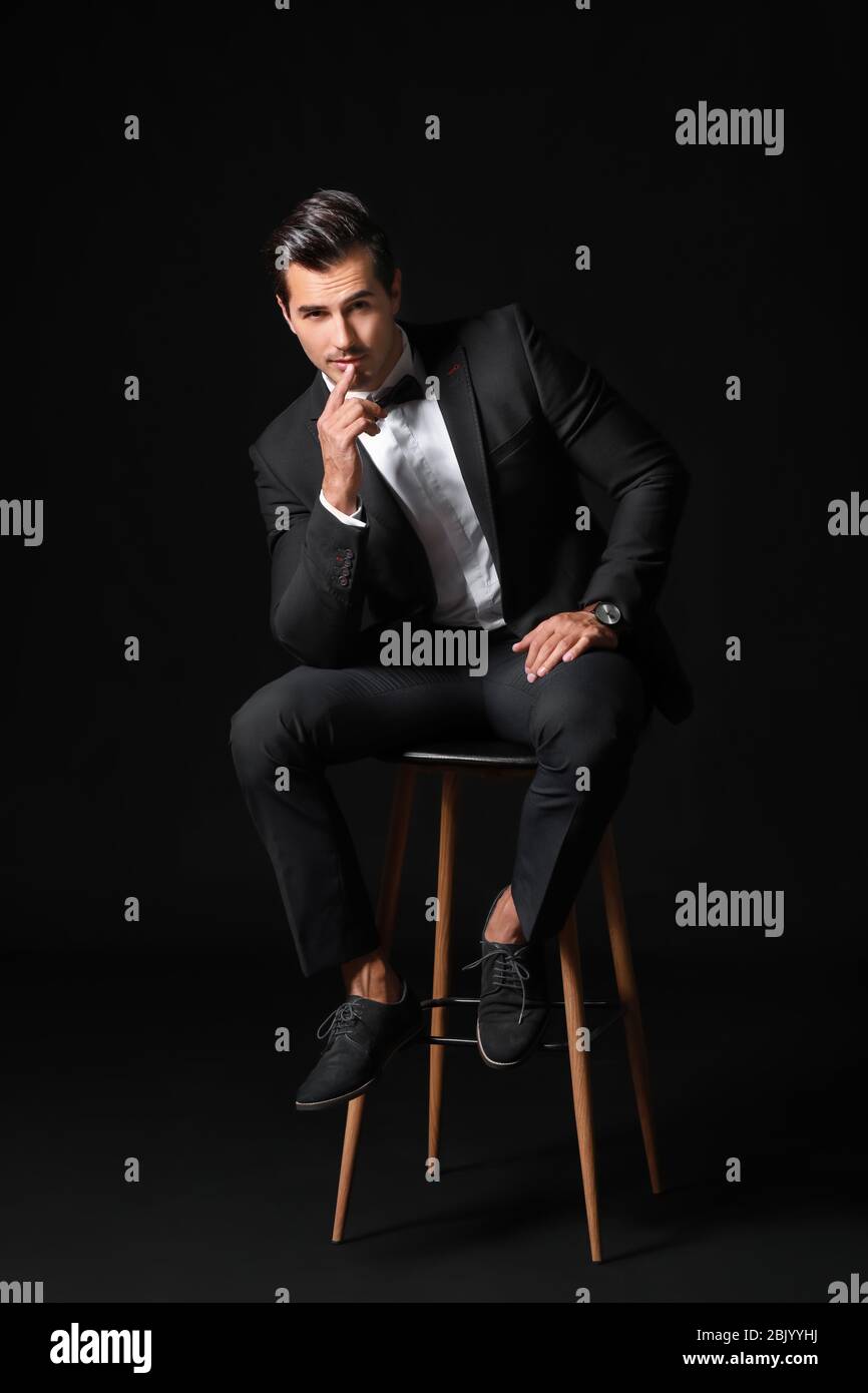 Fashionable man in formal clothes sitting on chair against dark ...