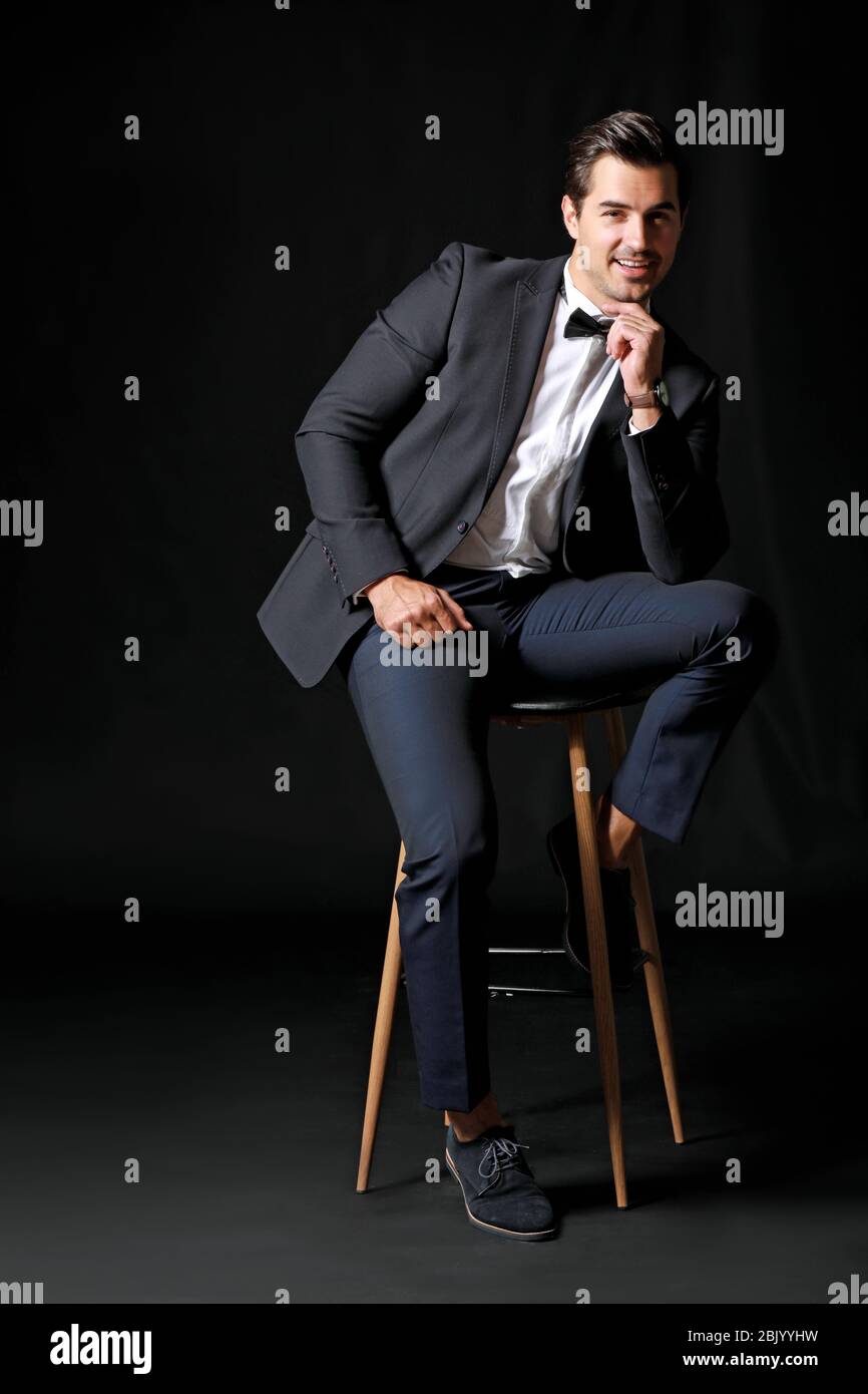 Fashionable man in formal clothes sitting on chair against dark ...