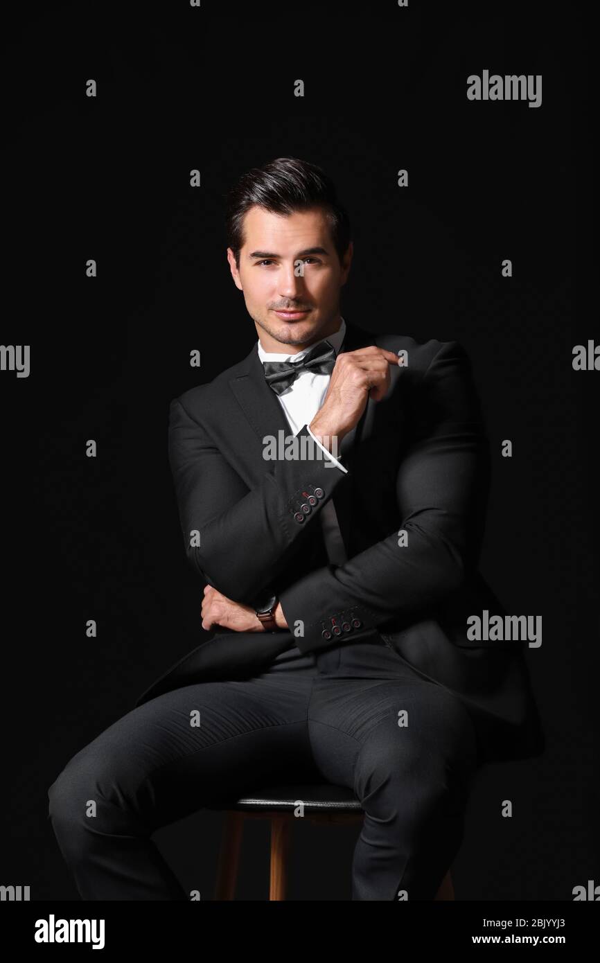 Fashionable man in formal clothes sitting on chair against dark ...