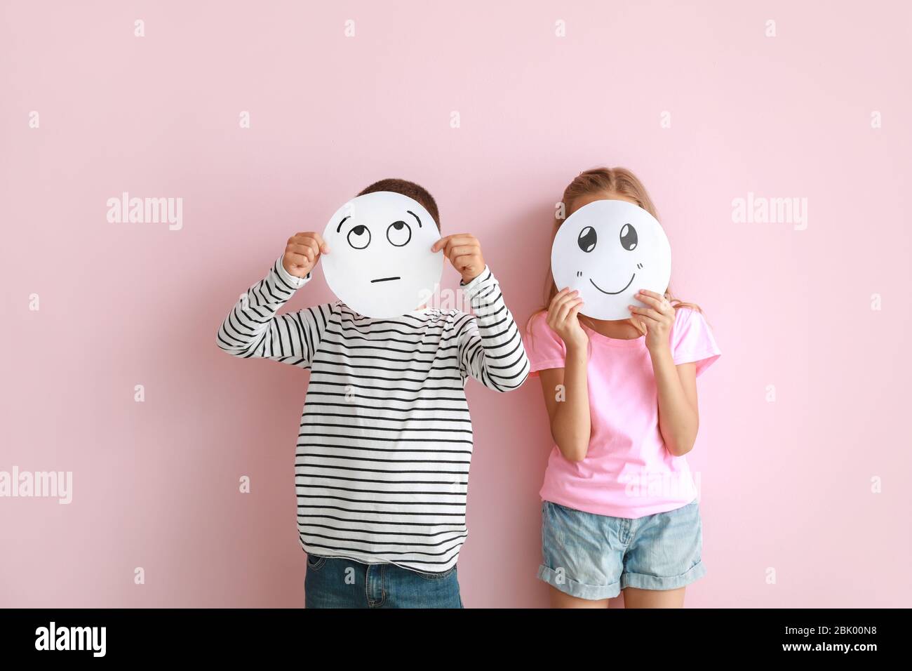 Little children hiding faces behind drawn emoticons on color background ...