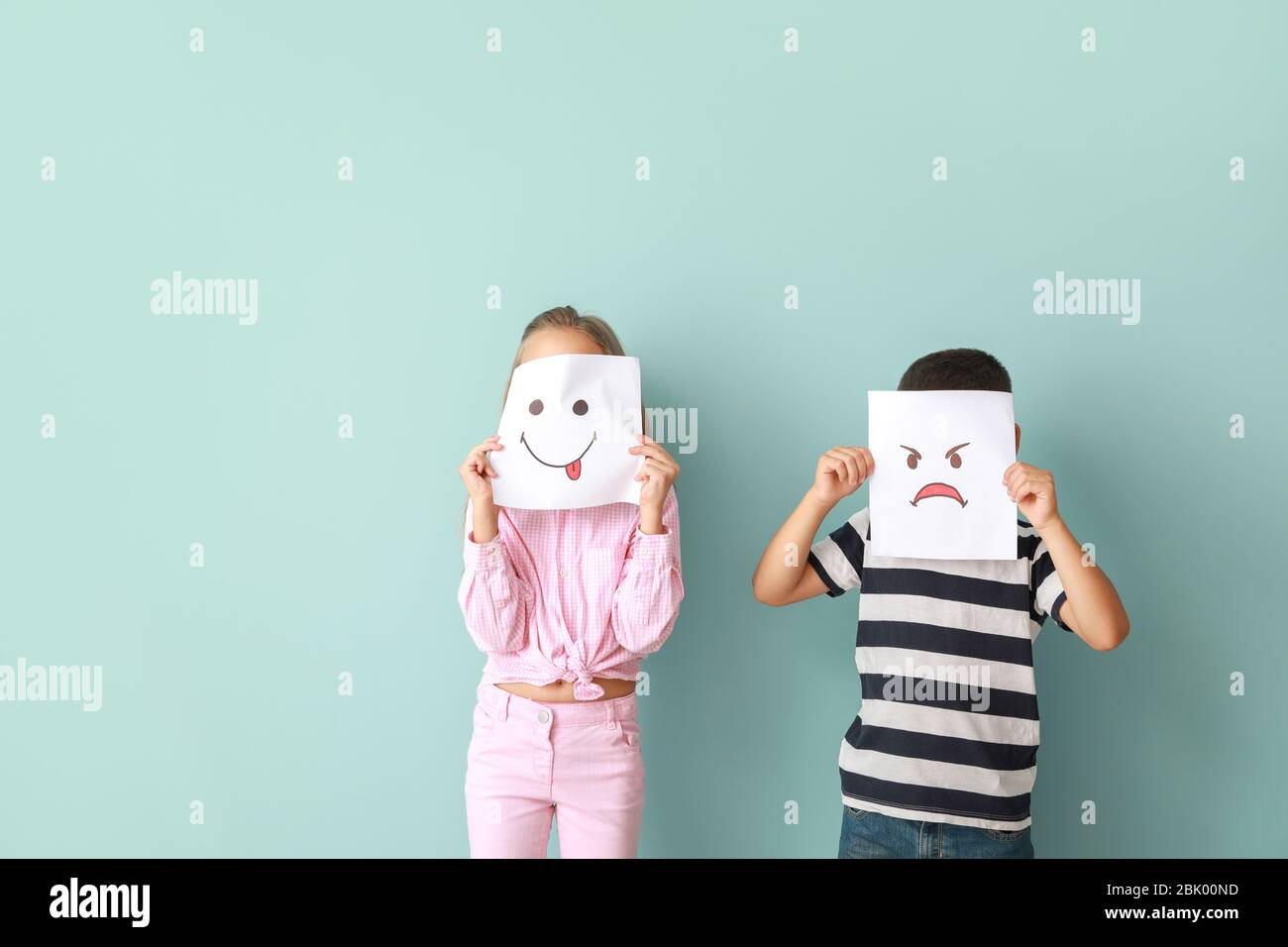 Little children hiding faces behind drawn emoticons on color background ...