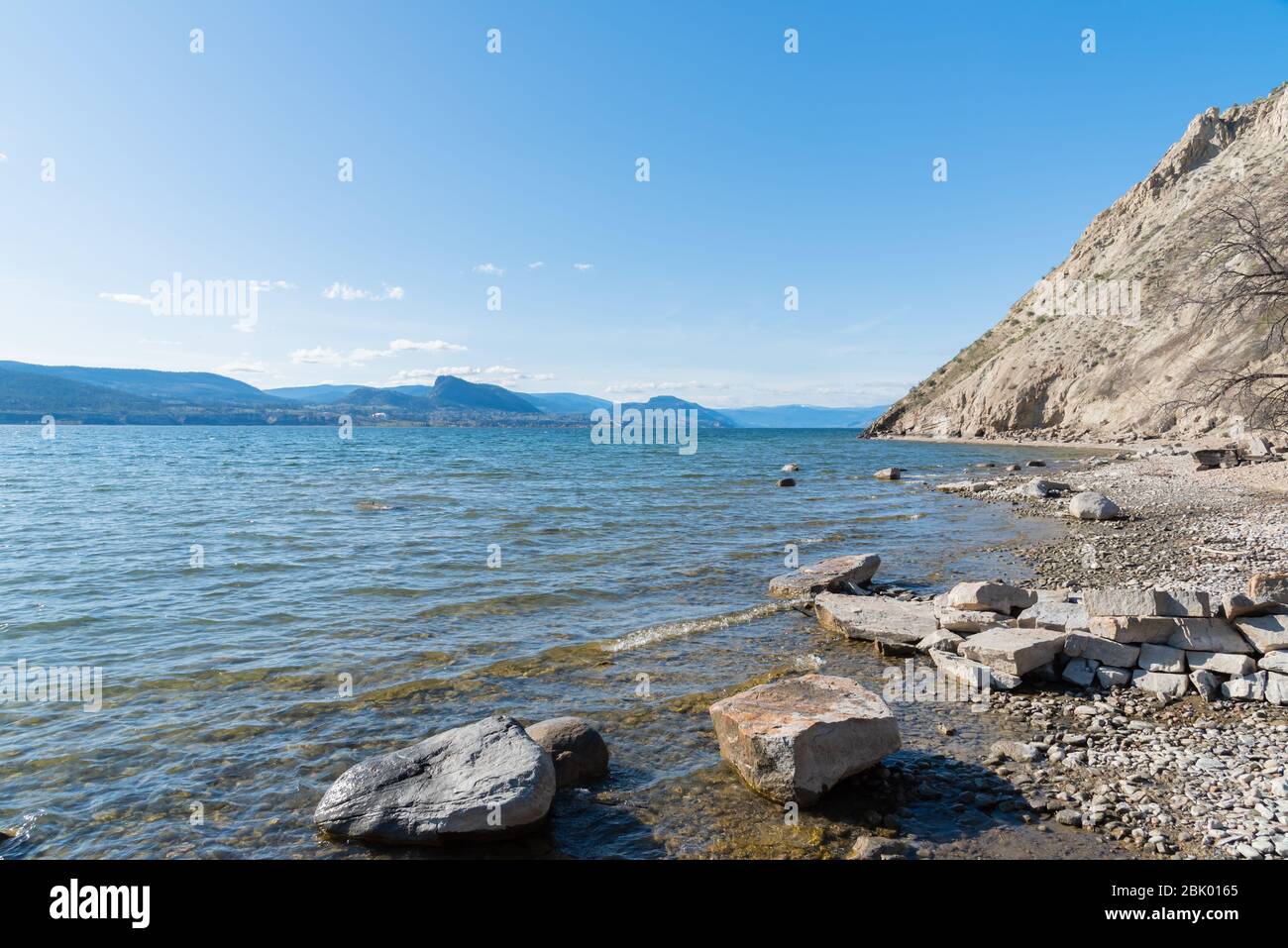 Rocky shoreline and sandstone cliffs on Okanagan Lake with view of blue ...