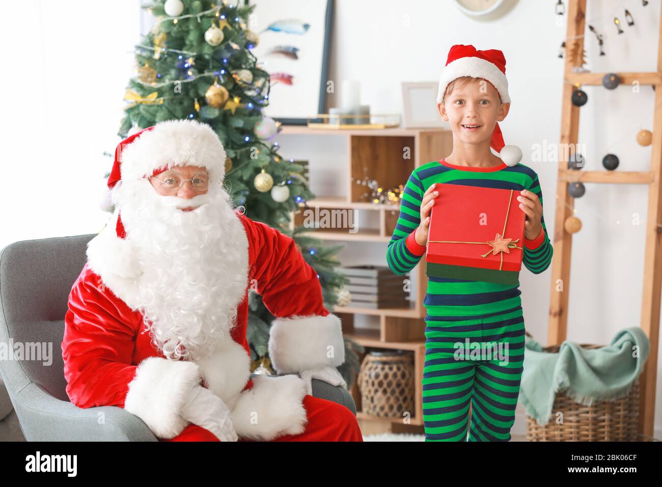 Santa Claus and little elf kid with gift in room decorated for ...