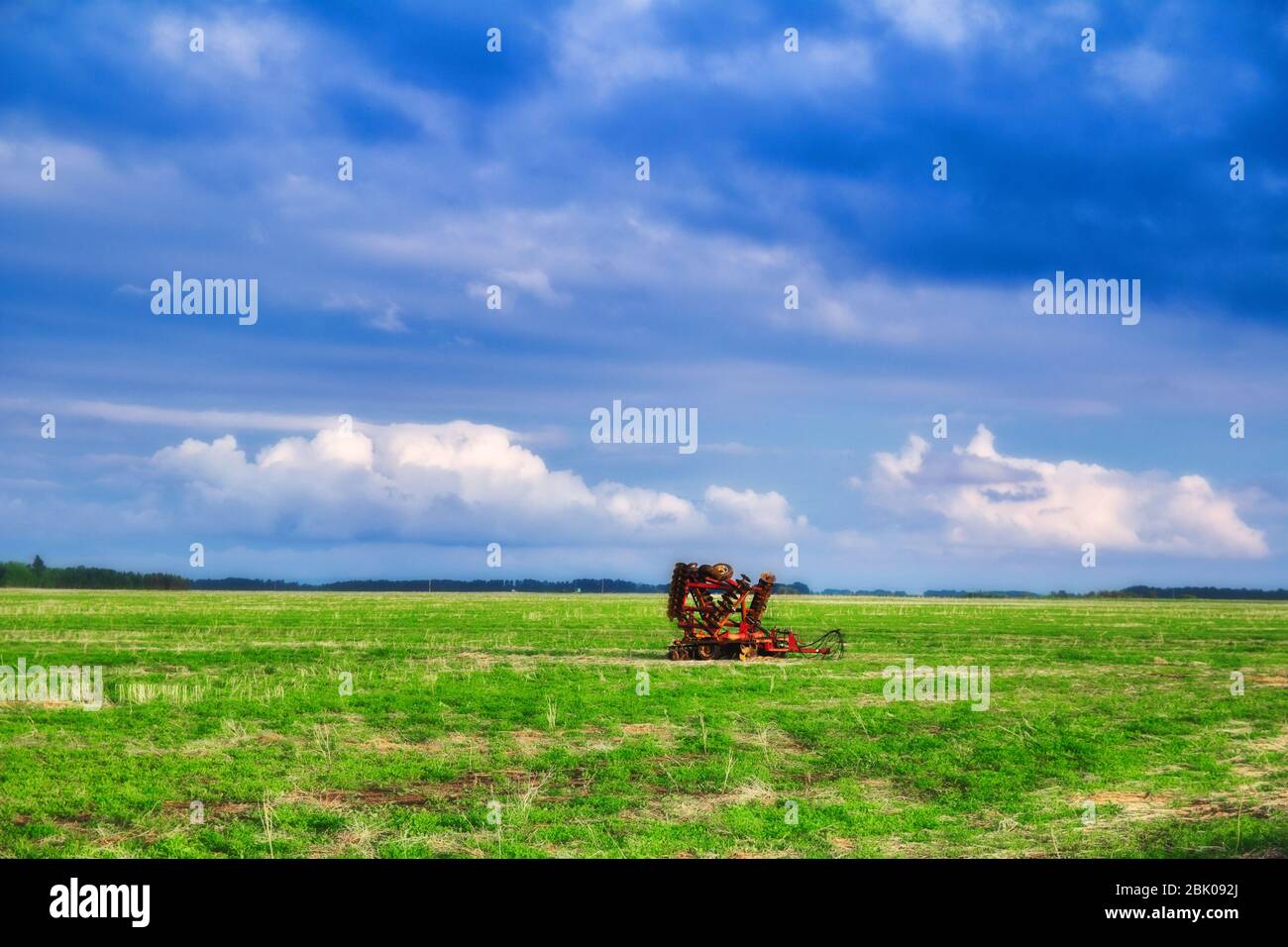 A folded up farm disc sitting on a green field under a blue stormy sky ...