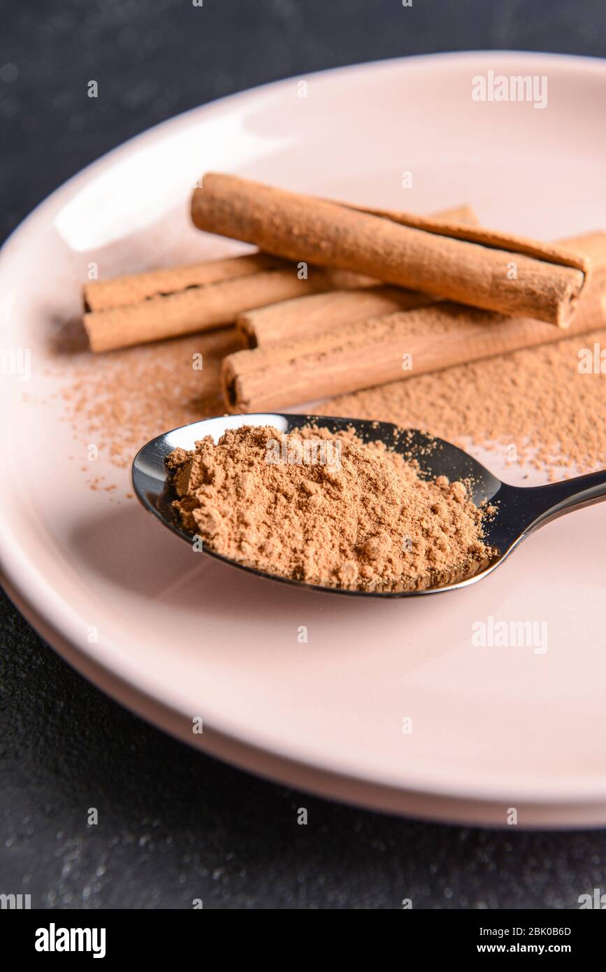 Spoon with cinnamon powder and sticks on plate, closeup Stock Photo - Alamy
