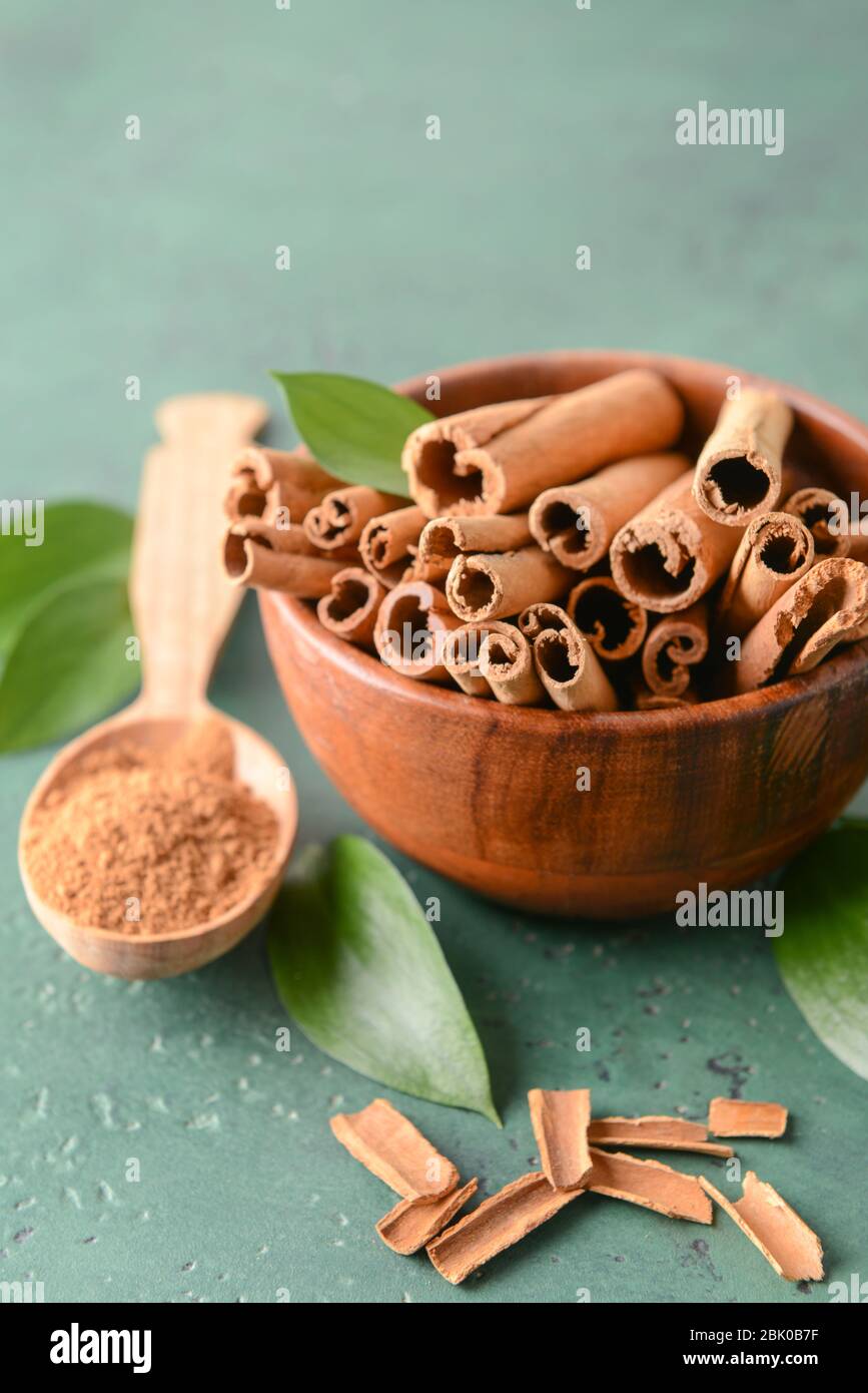 Bowl of aromatic cinnamon sticks and spoon with powder on color table ...