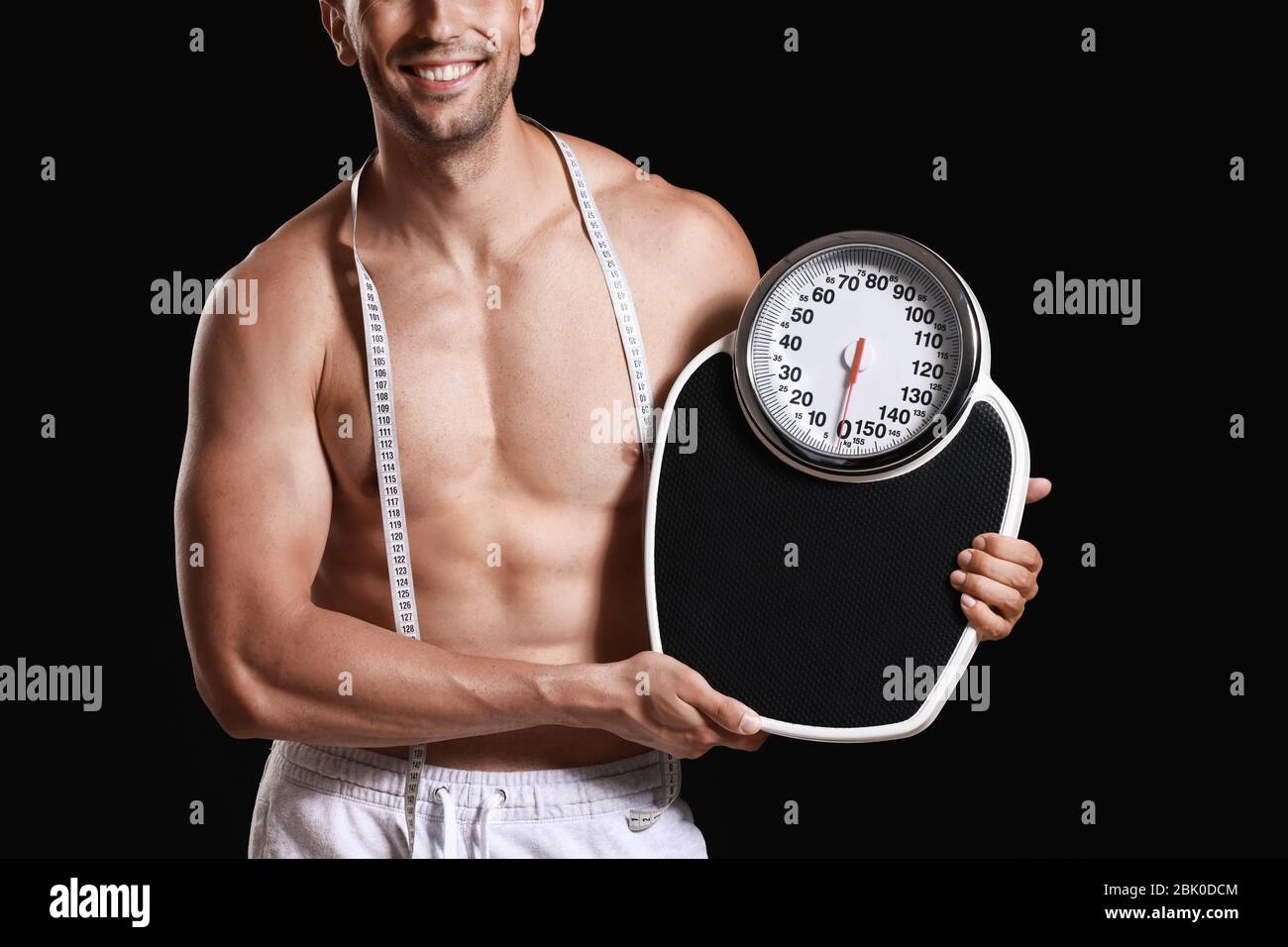 Handsome muscular man with measuring tape and scales on dark background ...