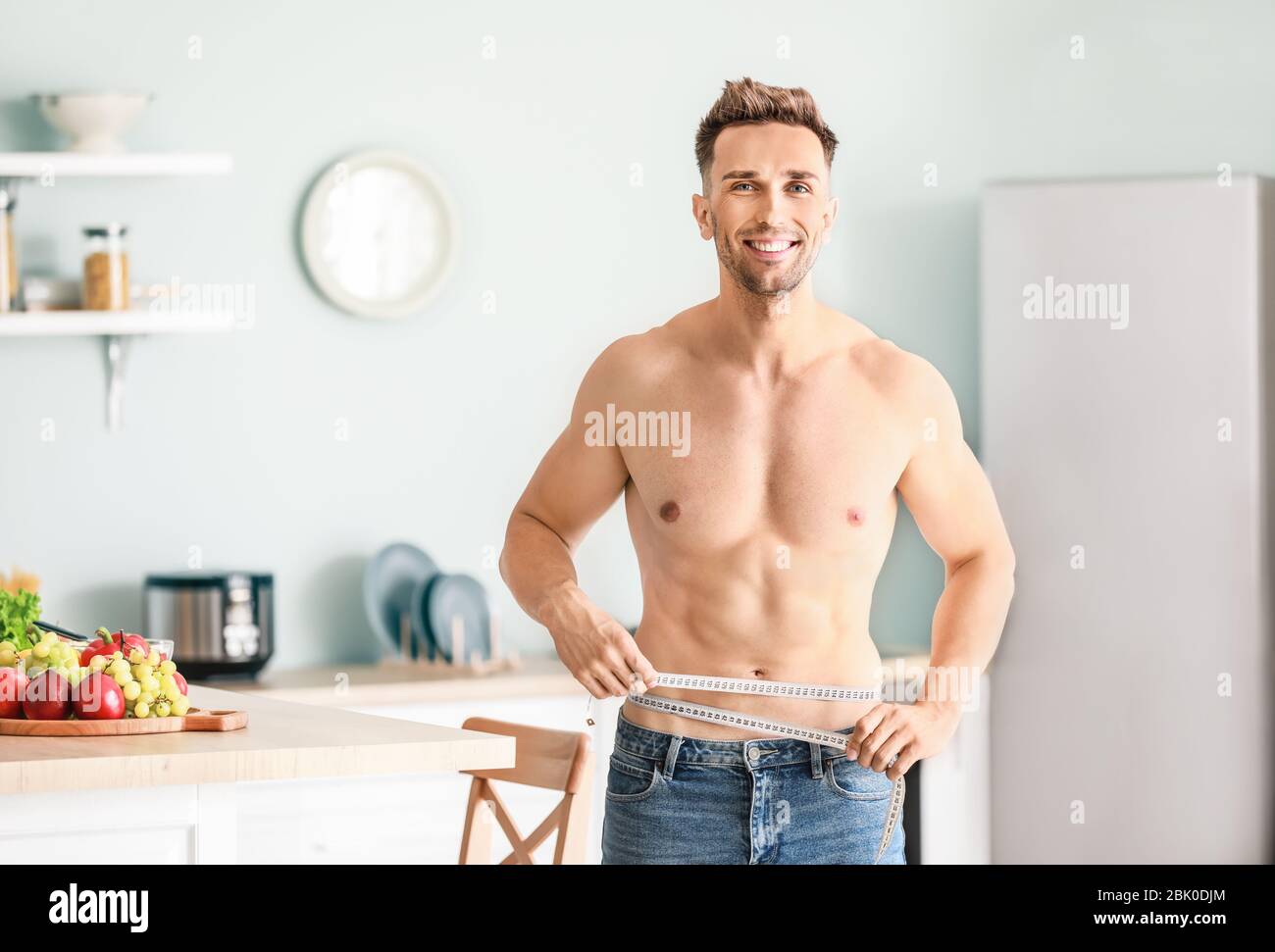 Handsome muscular man with measuring tape in kitchen. Weight loss ...