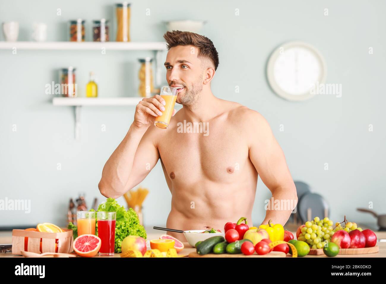 Handsome muscular man drinking juice in kitchen. Weight loss concept ...