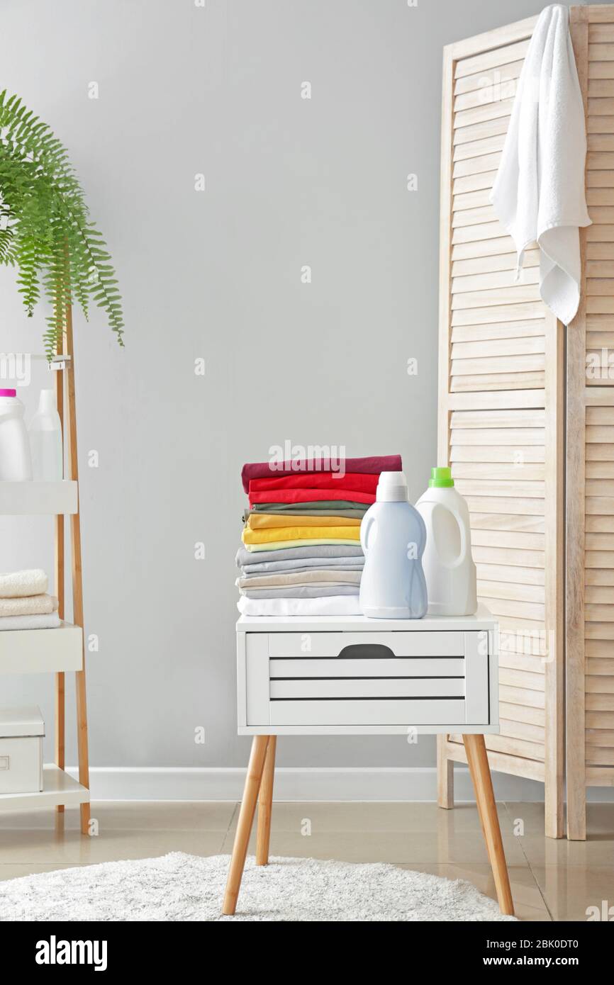 Stack of clean laundry and washing agents on table in bathroom Stock ...