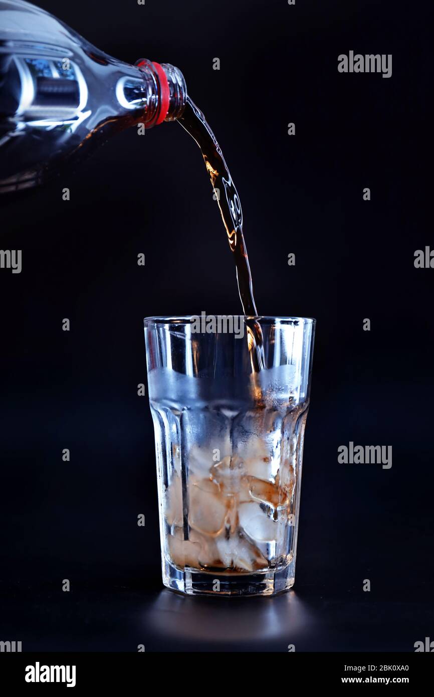 Pouring of cola into glass on dark background Stock Photo - Alamy