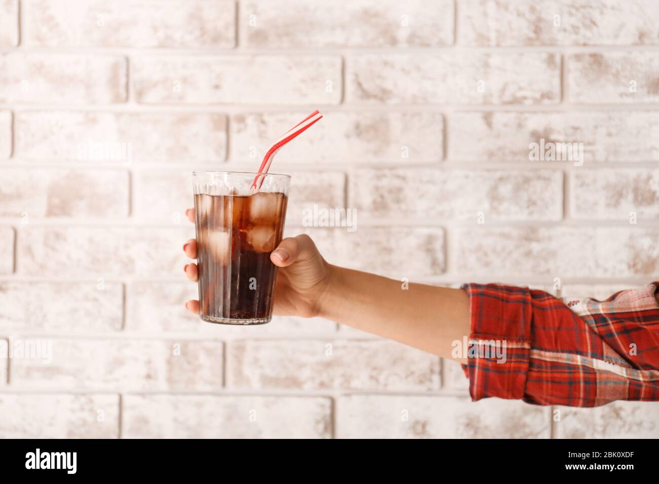 Female hand with glass of cold cola against brick wall Stock Photo - Alamy