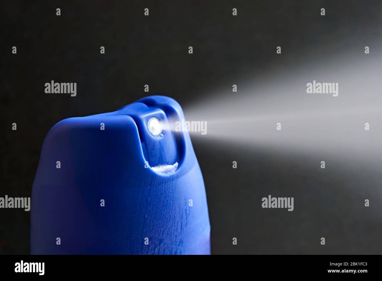 Closeup of blue spray bottle or can and spraying mist against a dark ...