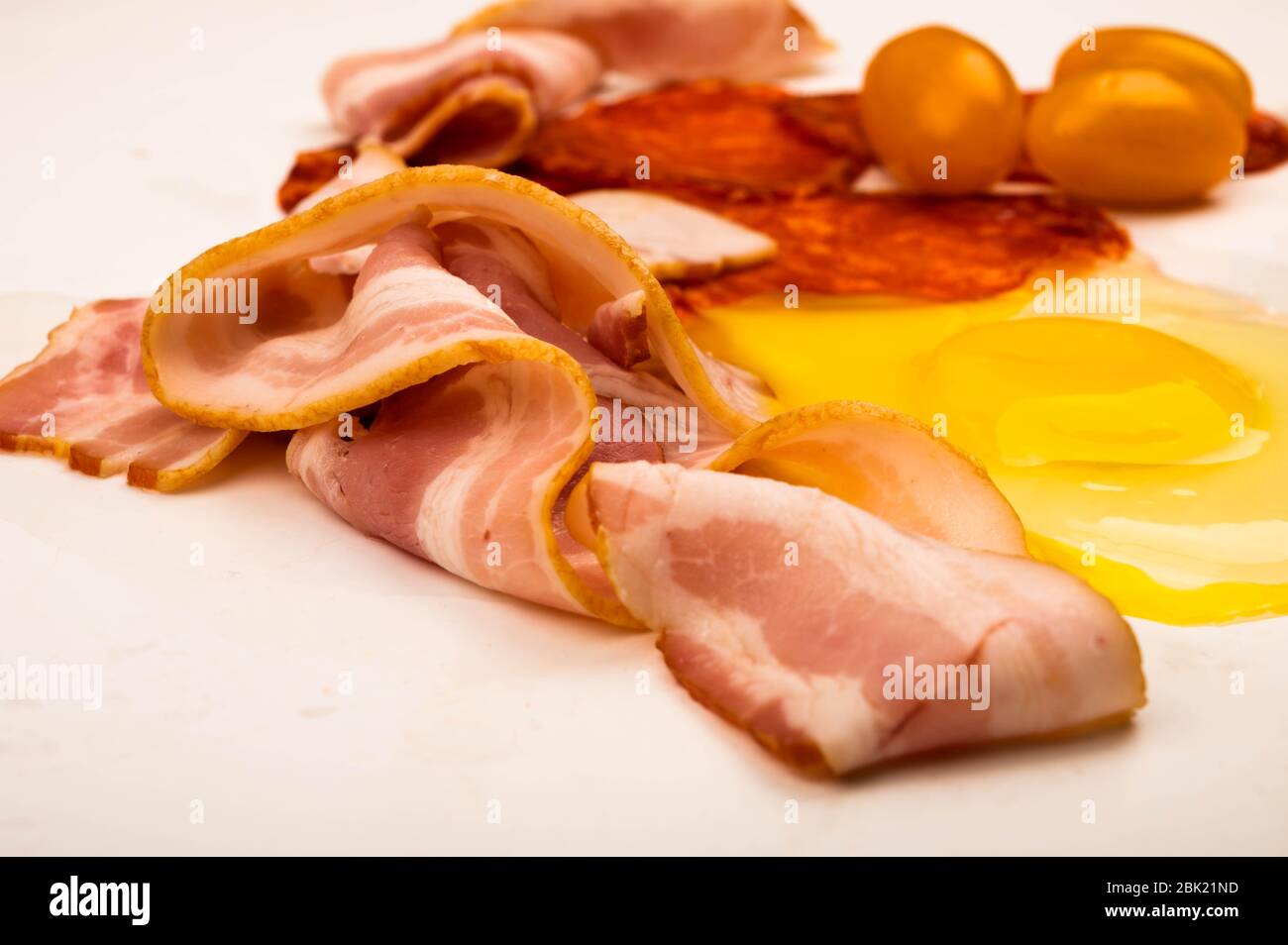 A broken chicken egg without a shell, slices of sausage and bacon and ...