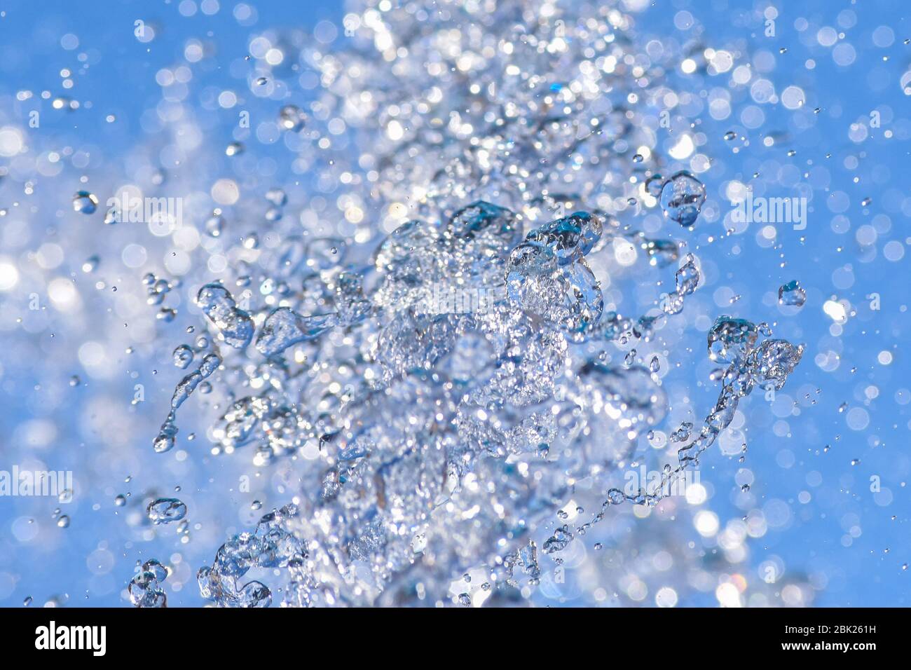 Water droplets spraying from a fountain in abstract design on blue sky ...
