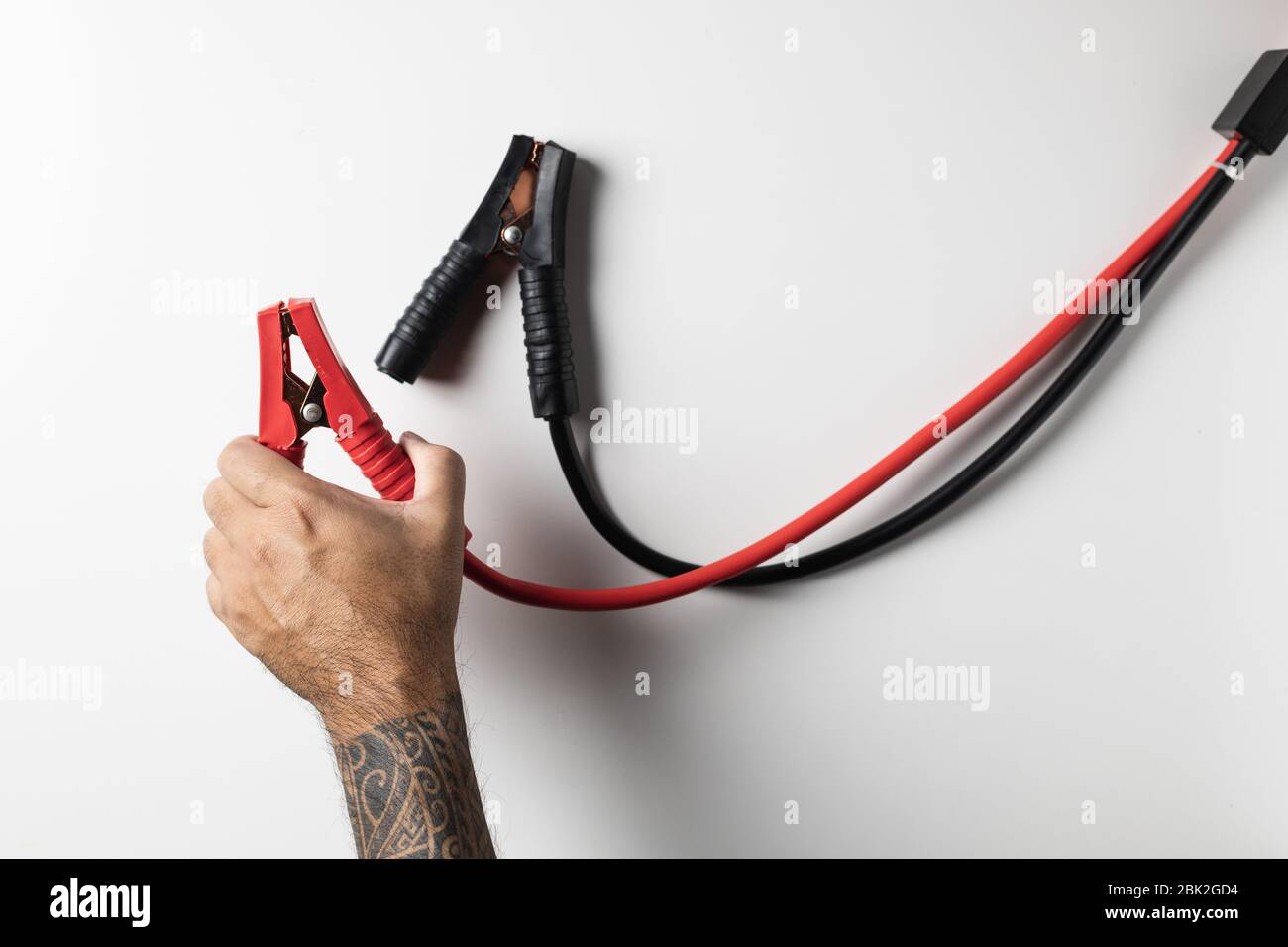 Man hand with tattoo holding red jumper cable isolated on white ...