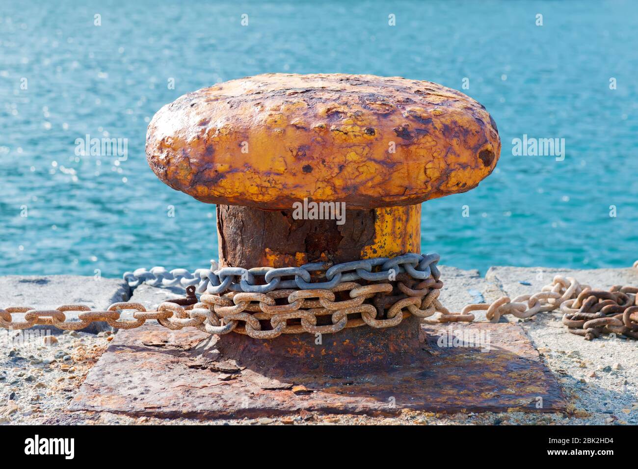 big oarange old rusty mooring bitt on a dock , blue water background ...