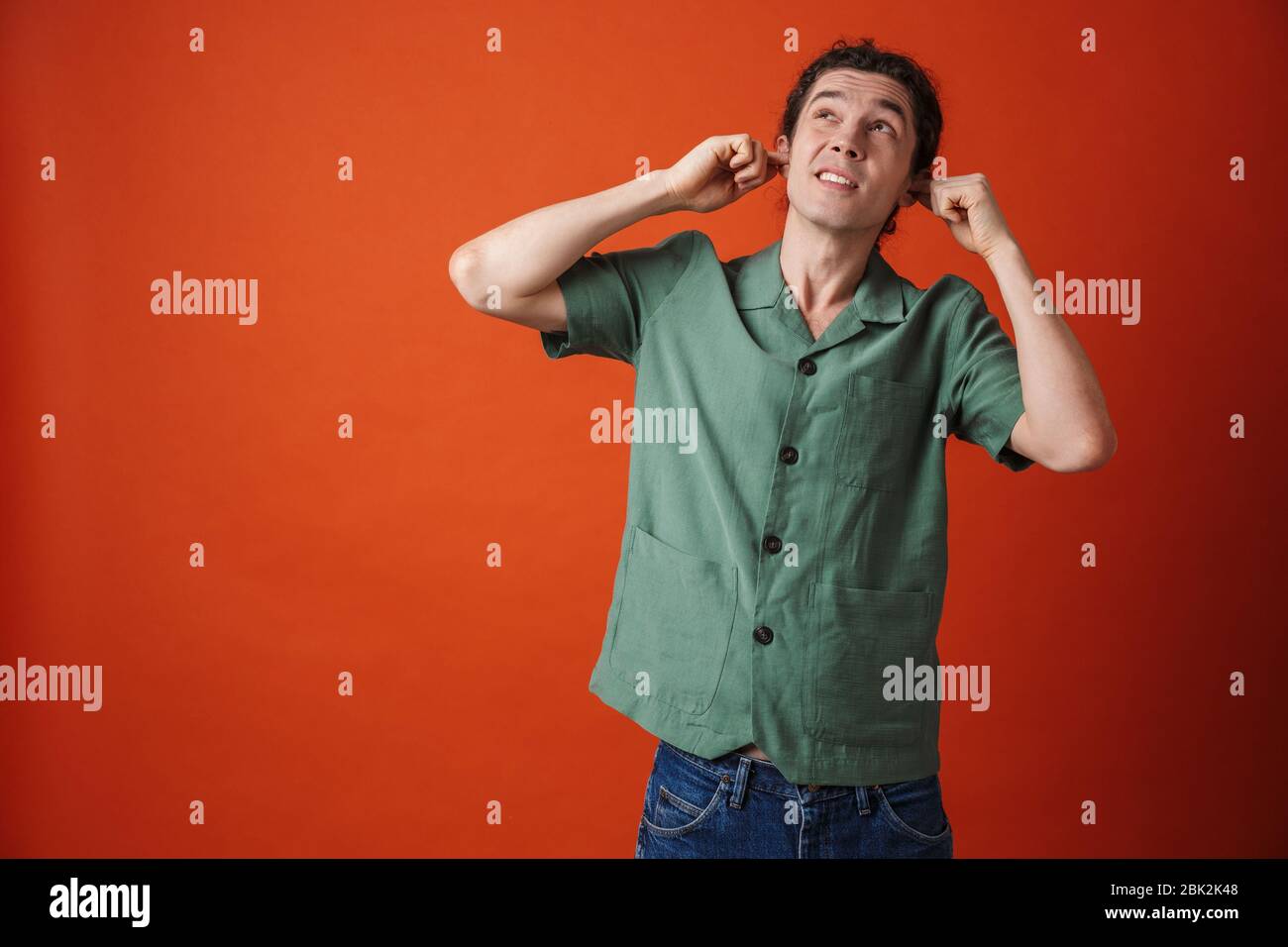 Image of displeased handsome man looking upward and plugging his ears ...