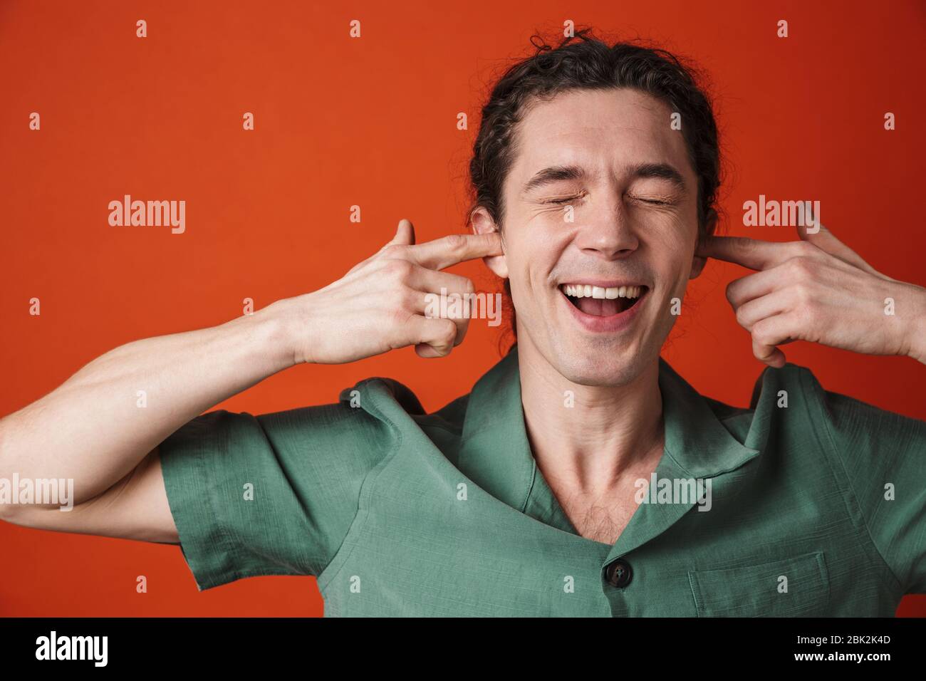 Image of happy handsome man laughing and plugging his ears isolated ...
