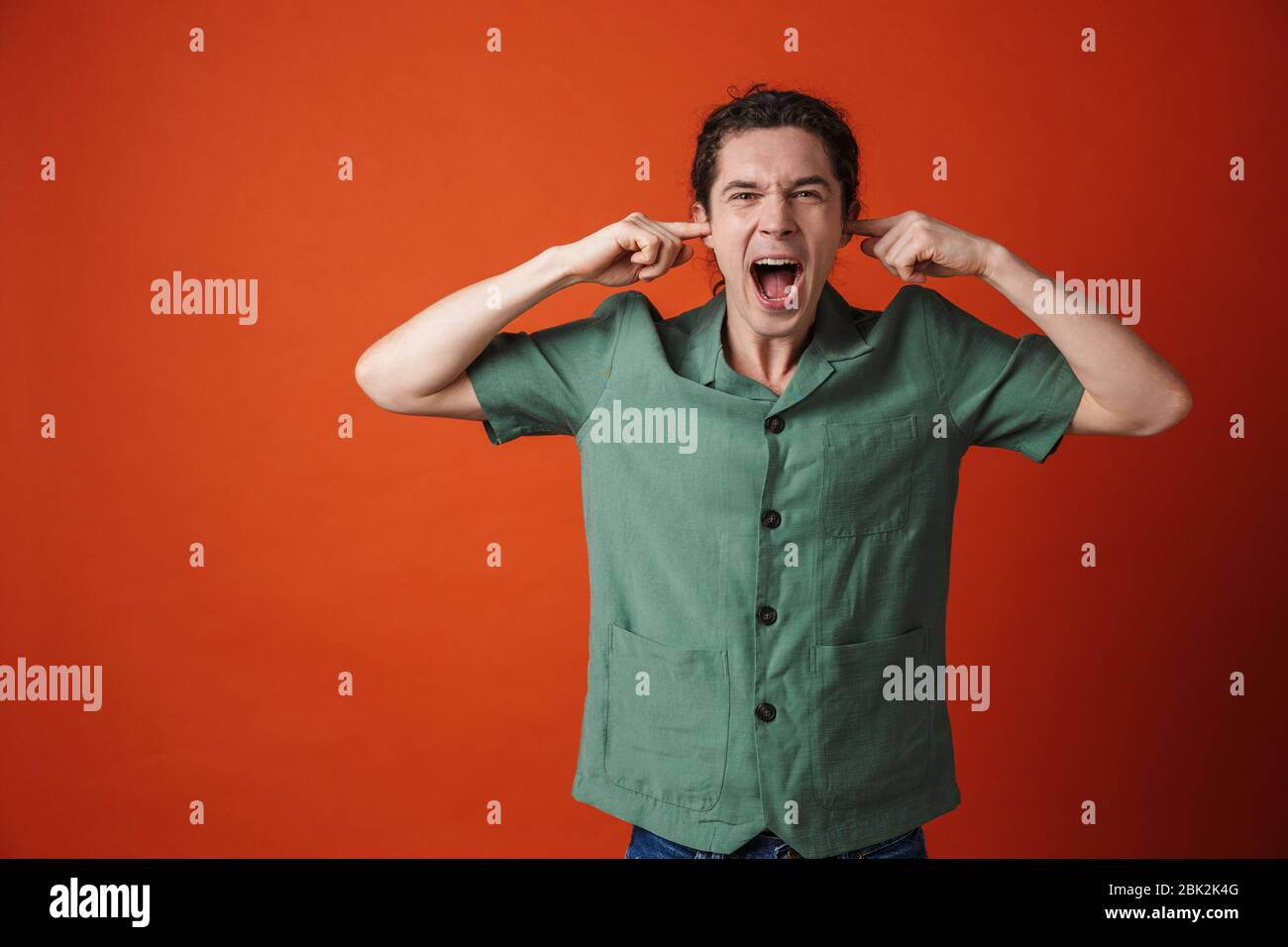 Image of annoyed handsome man screaming at camera and plugging his ears ...