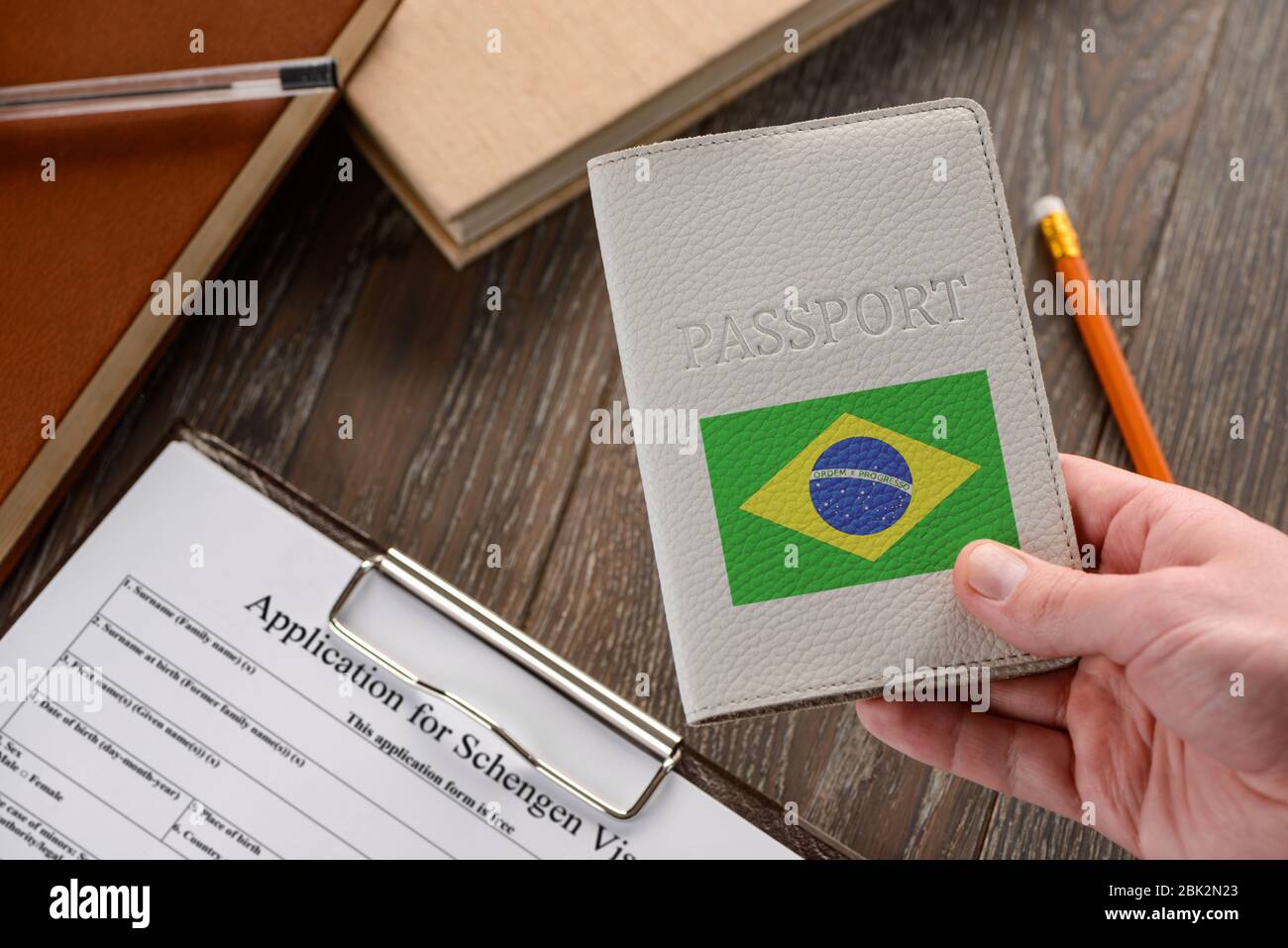 Hand holding a Brazilian passport, an application form in background ...