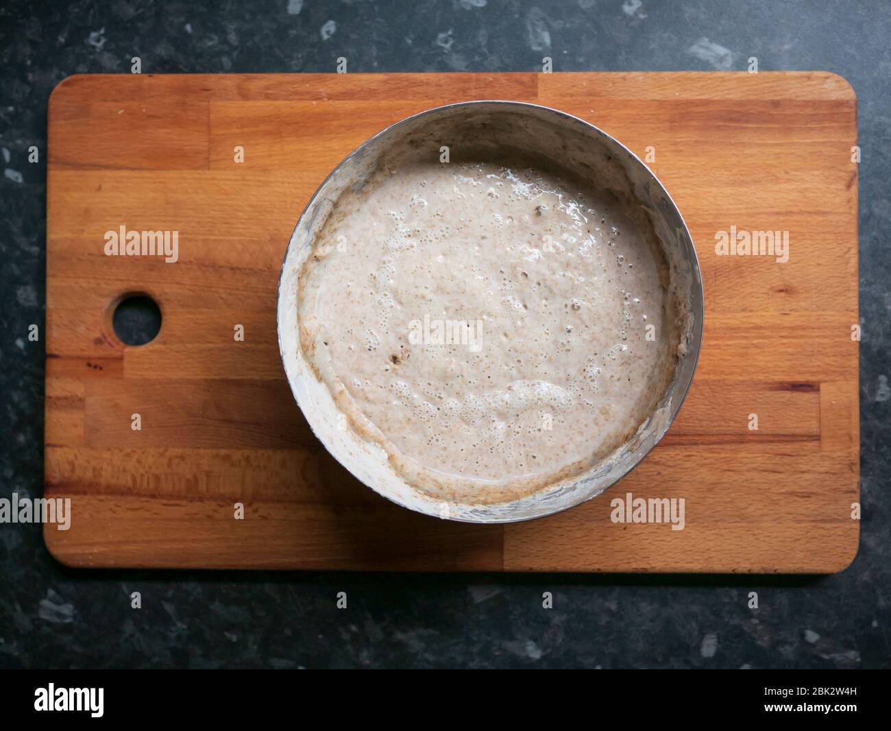 A top down view of a bubbling sourdough starter on a chopping board ...