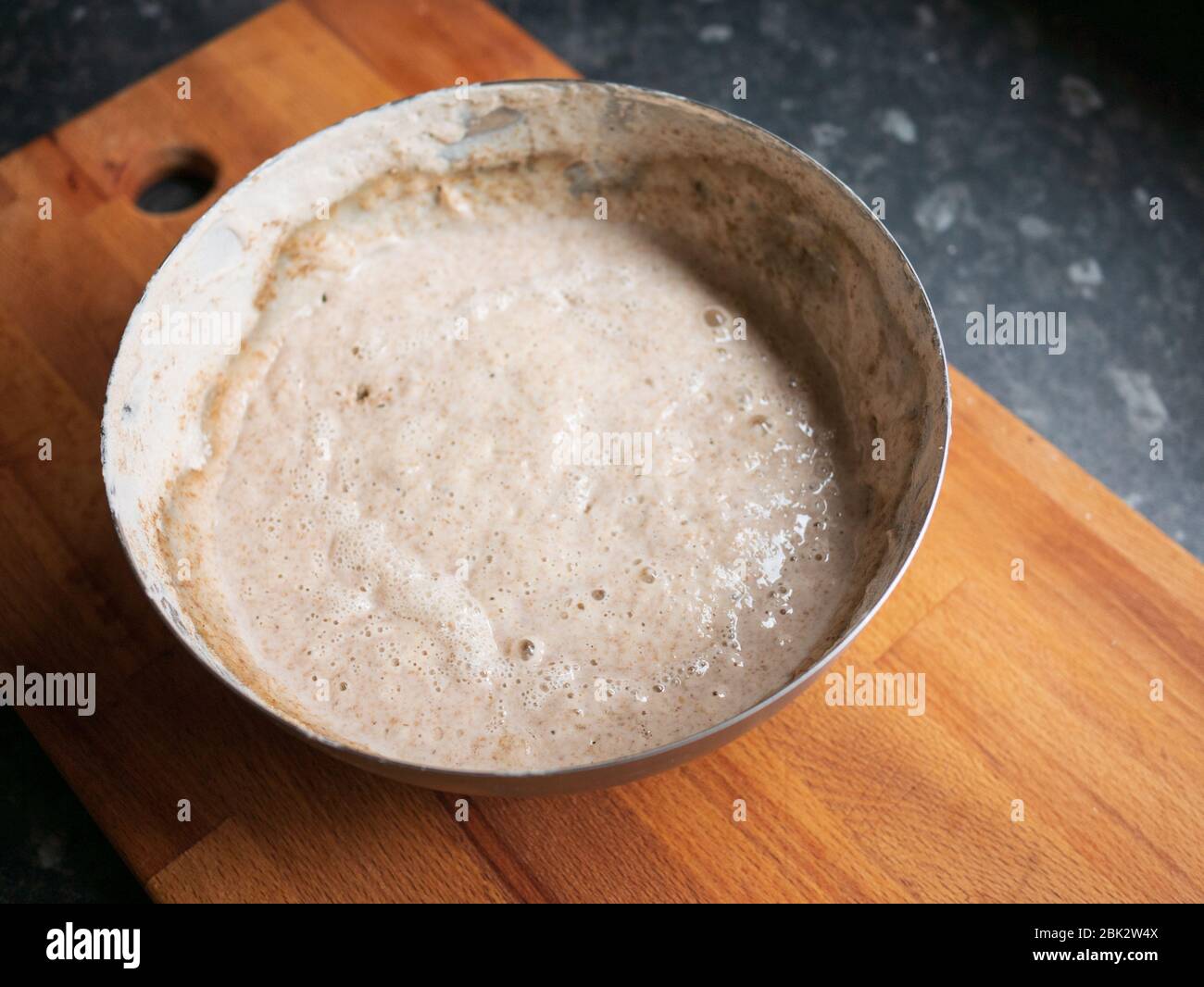 A top down view of a bubbling sourdough starter on a chopping board ...