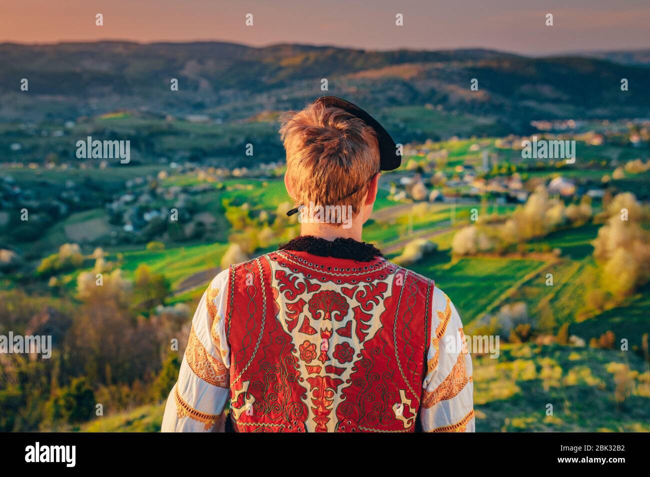 A young man in a Slovak folk costume looks at the spring landscape in ...