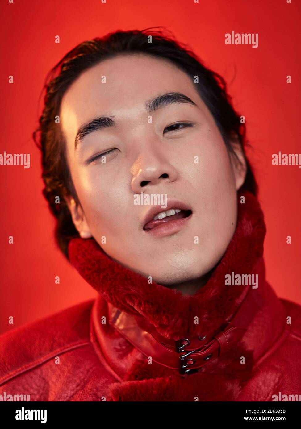 funny Asian man in red clothes on a red background with one eye closed ...