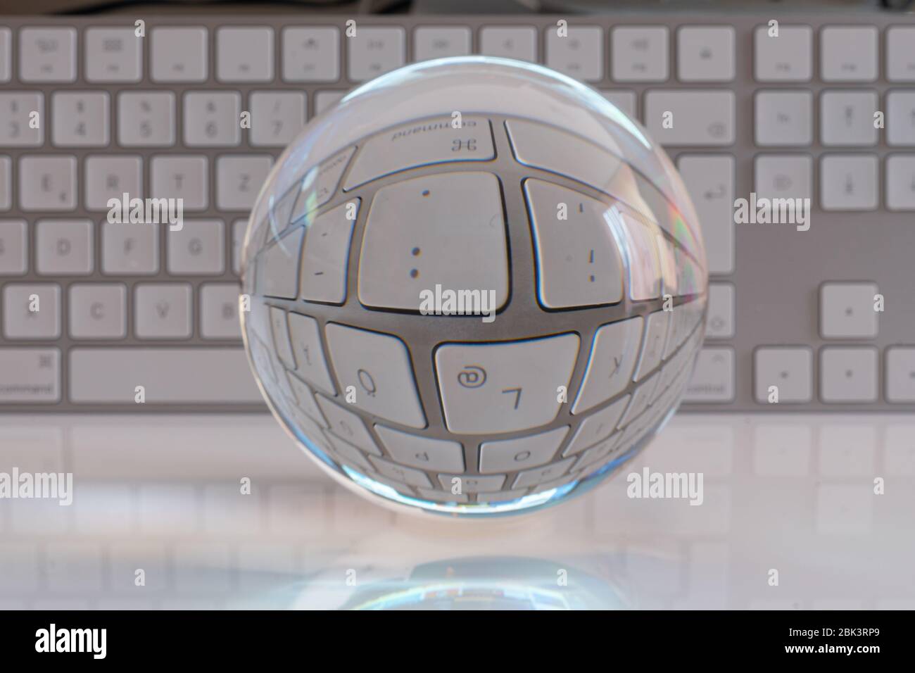 a crystal-clear glass ball stands in front of a white computer keyboard ...
