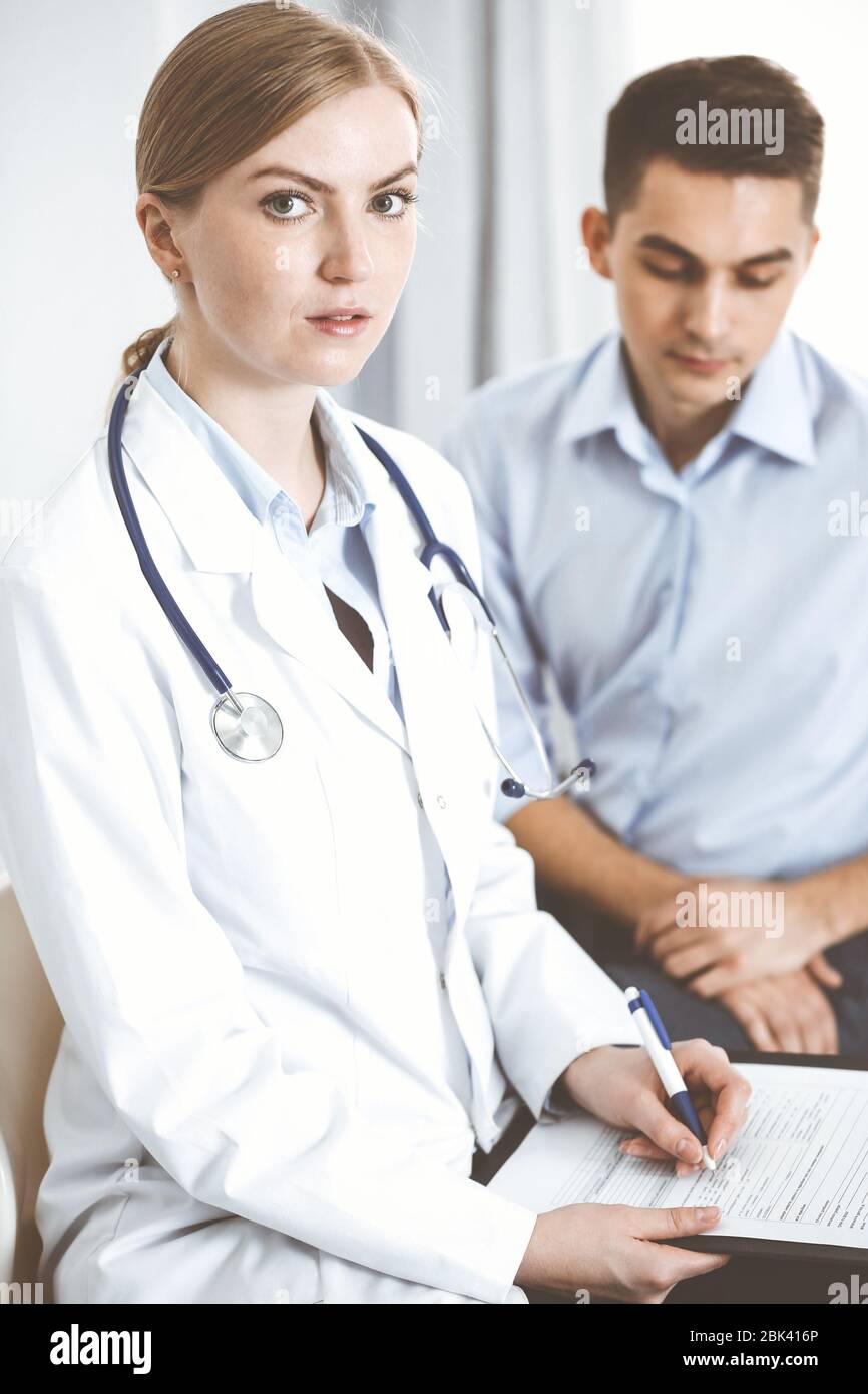 Female doctor holding application form while consulting man patient in ...