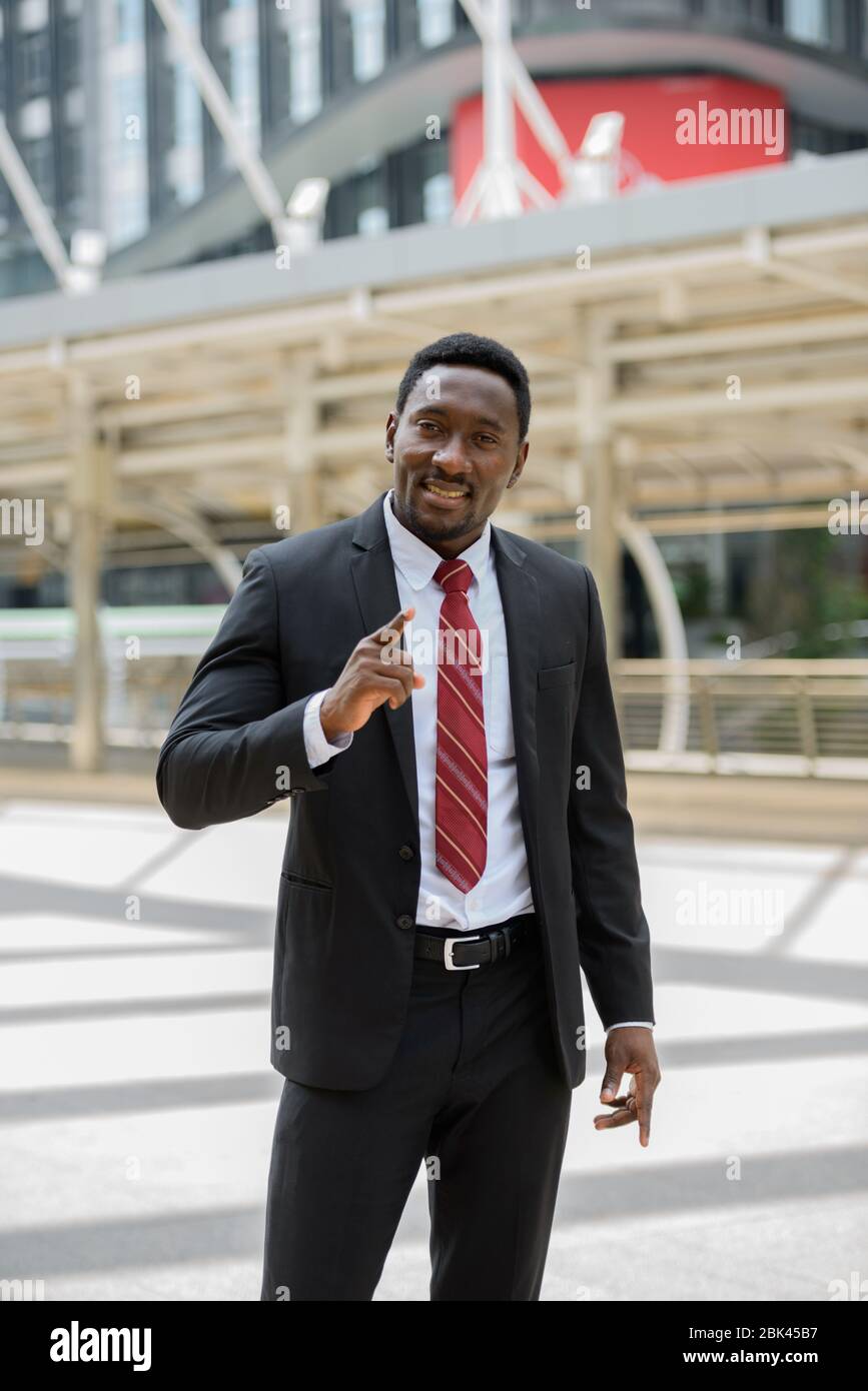 Happy young African businessman pointing finger in the city outdoors ...