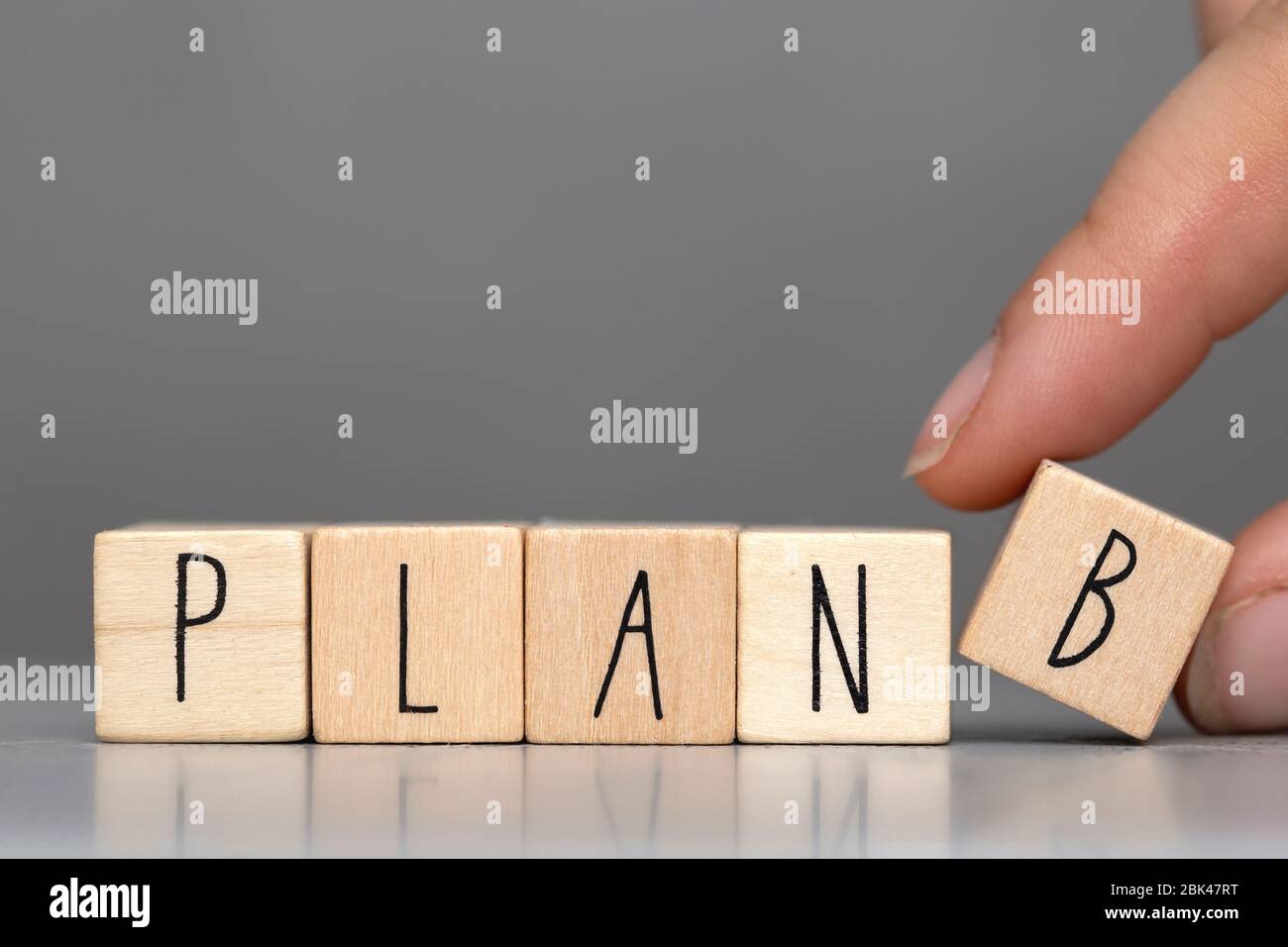 Wooden cubes with the word Plan B on grey background and human finger ...