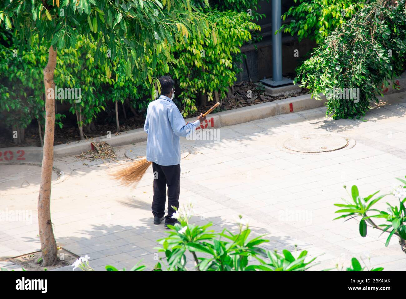 Male sweeper in blue uniform cleaning street and sidewalks with long ...