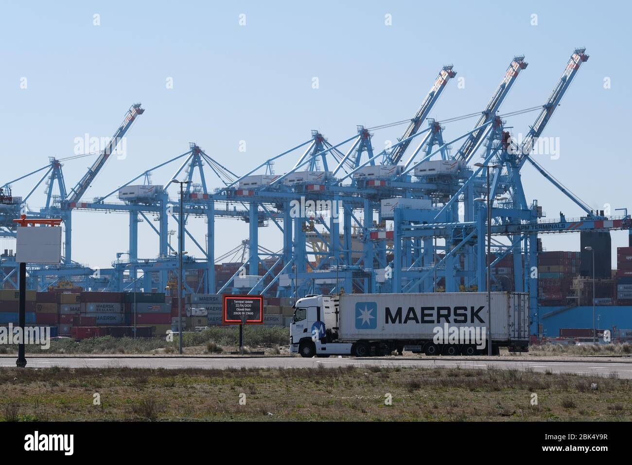 A truck carrying a shipping container passes cranes standing at the ...