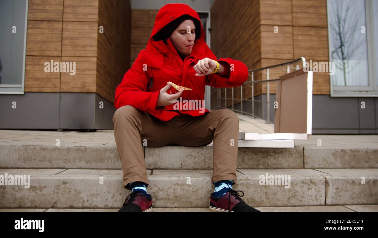 A man in red clothes eating pizza sitting on the border and watching at ...
