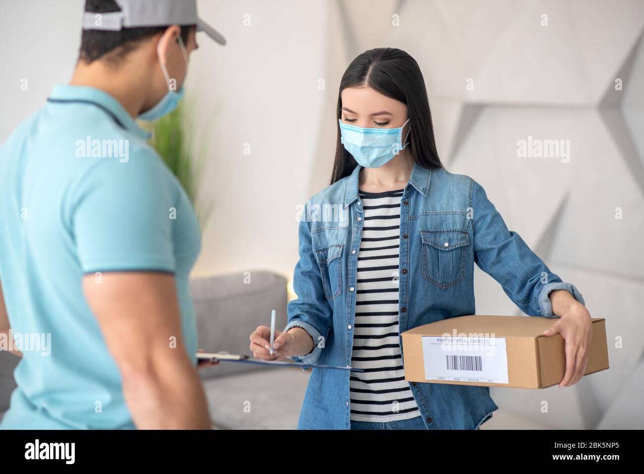 Woman with a parcel signing a man-held document Stock Photo - Alamy