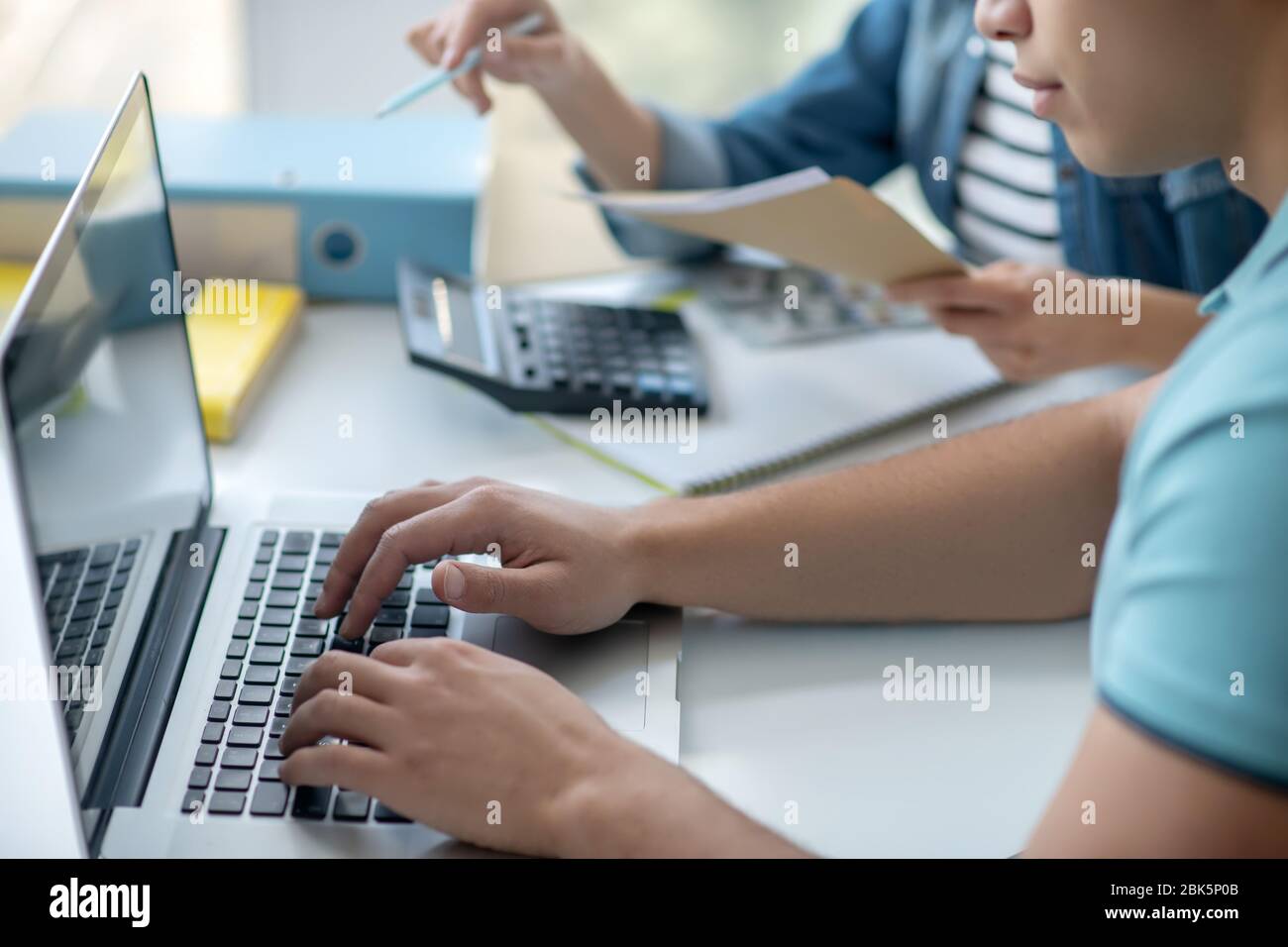 Male hands typing on laptop, female hands holding pen and papers Stock ...